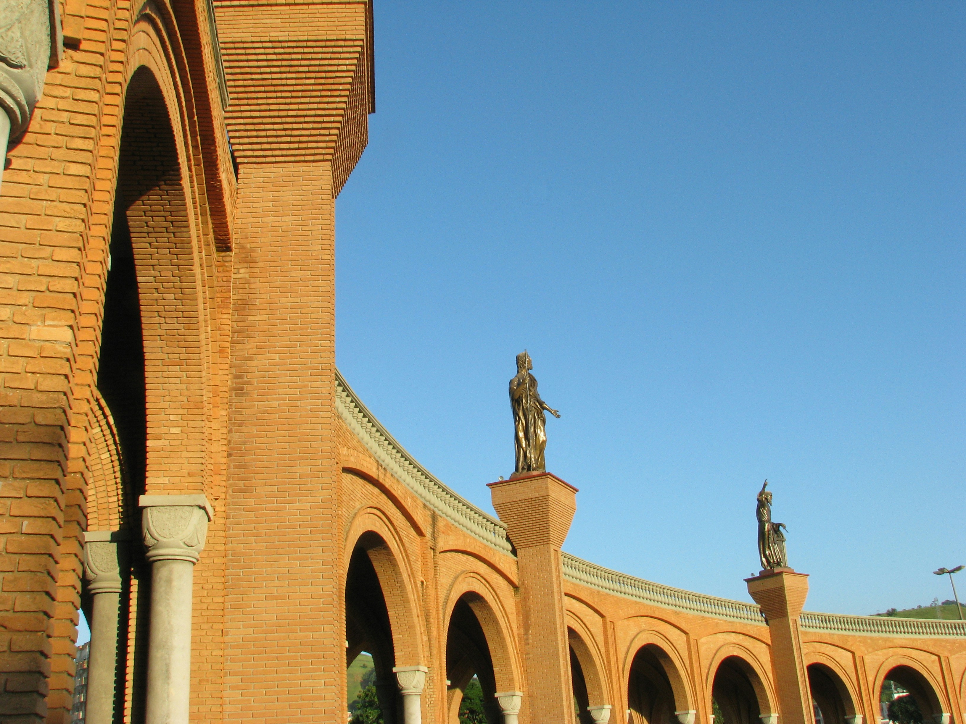 Curved brick arches adorned with statues against a clear blue sky.