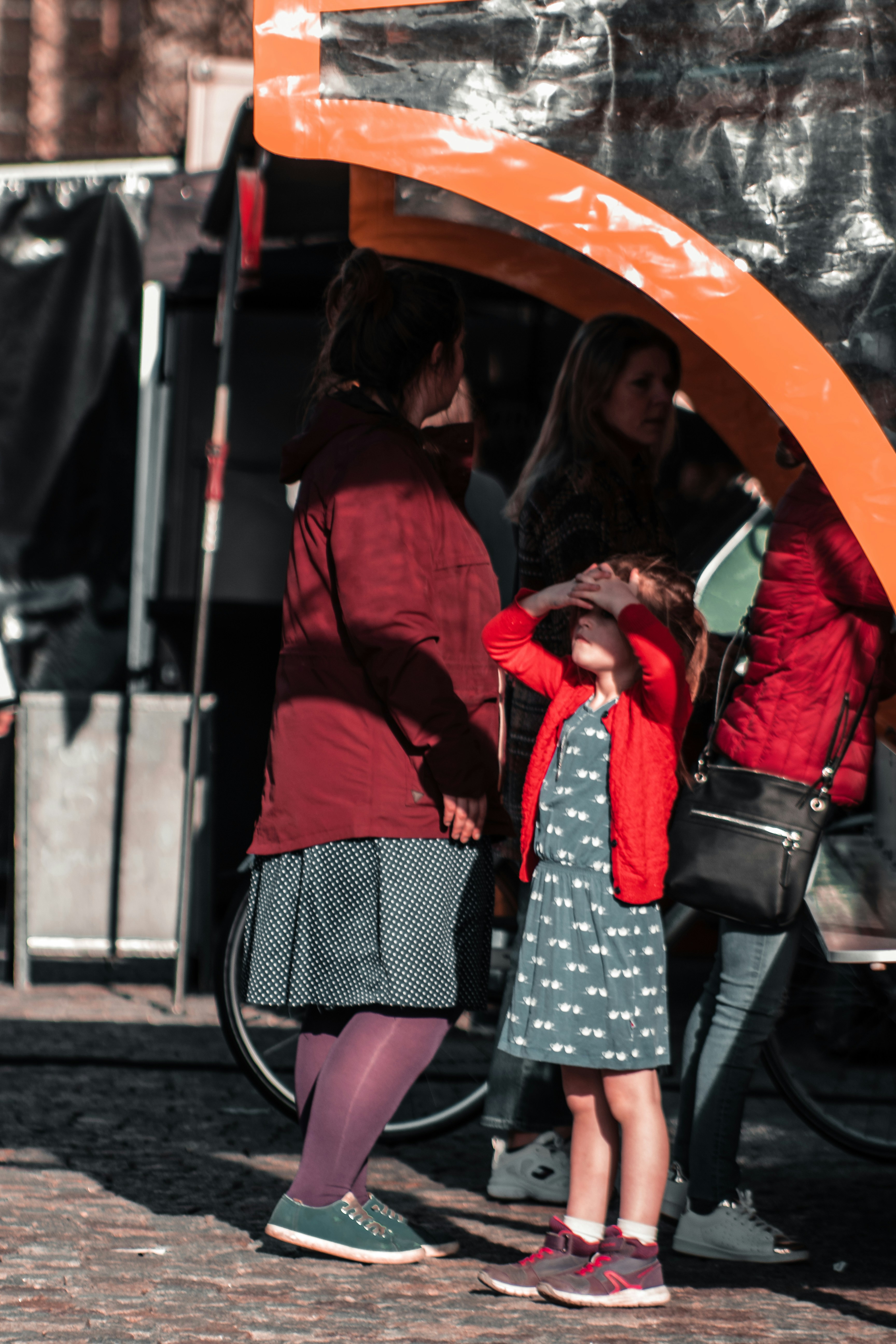 Sunlit Moment Under the Arch: A Little Girl Shields Her Eyes Amid Midsummer Streets