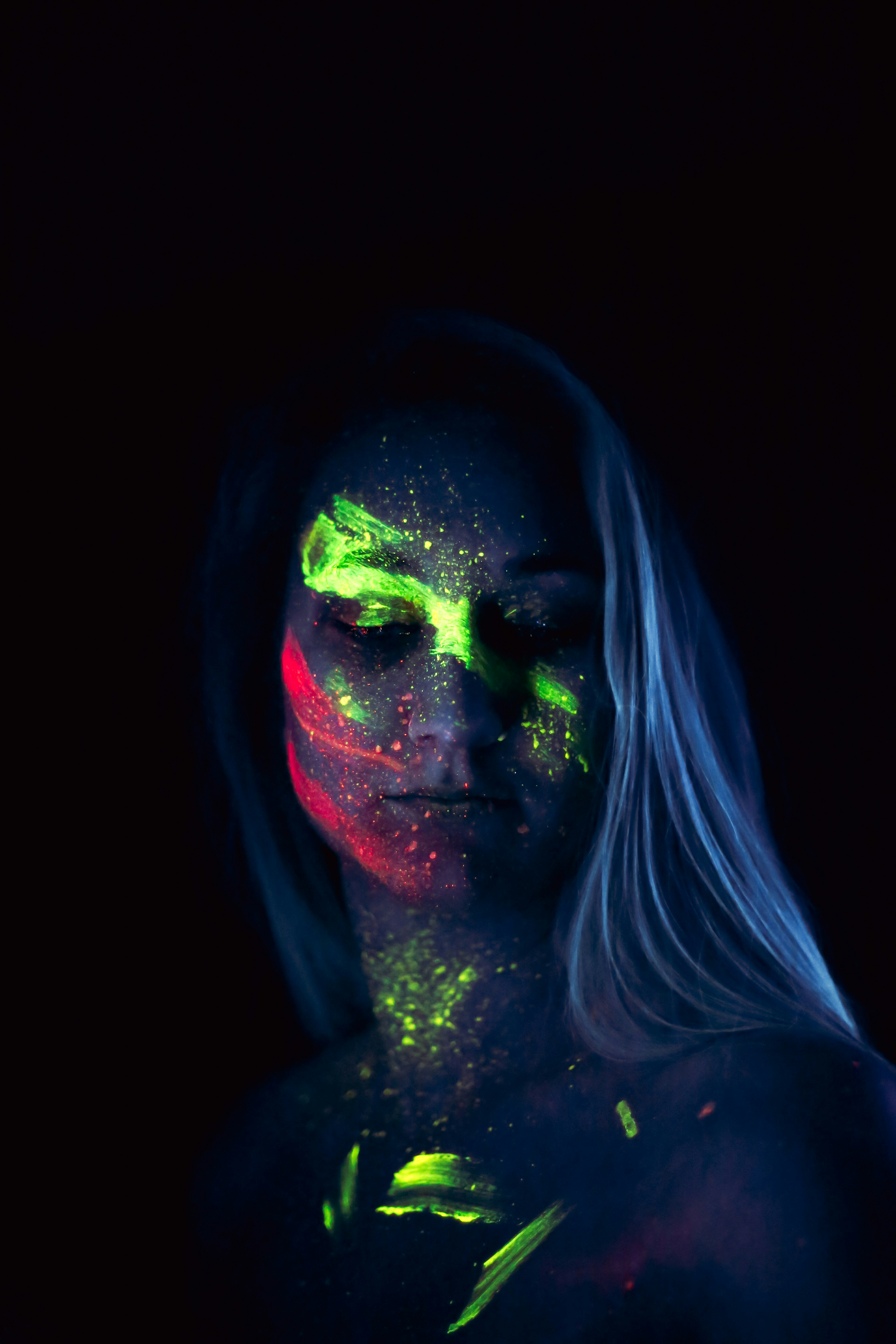 Model adorned with vibrant neon face paint against a dark backdrop, creating a striking contrast that highlights the artistry of body paint.