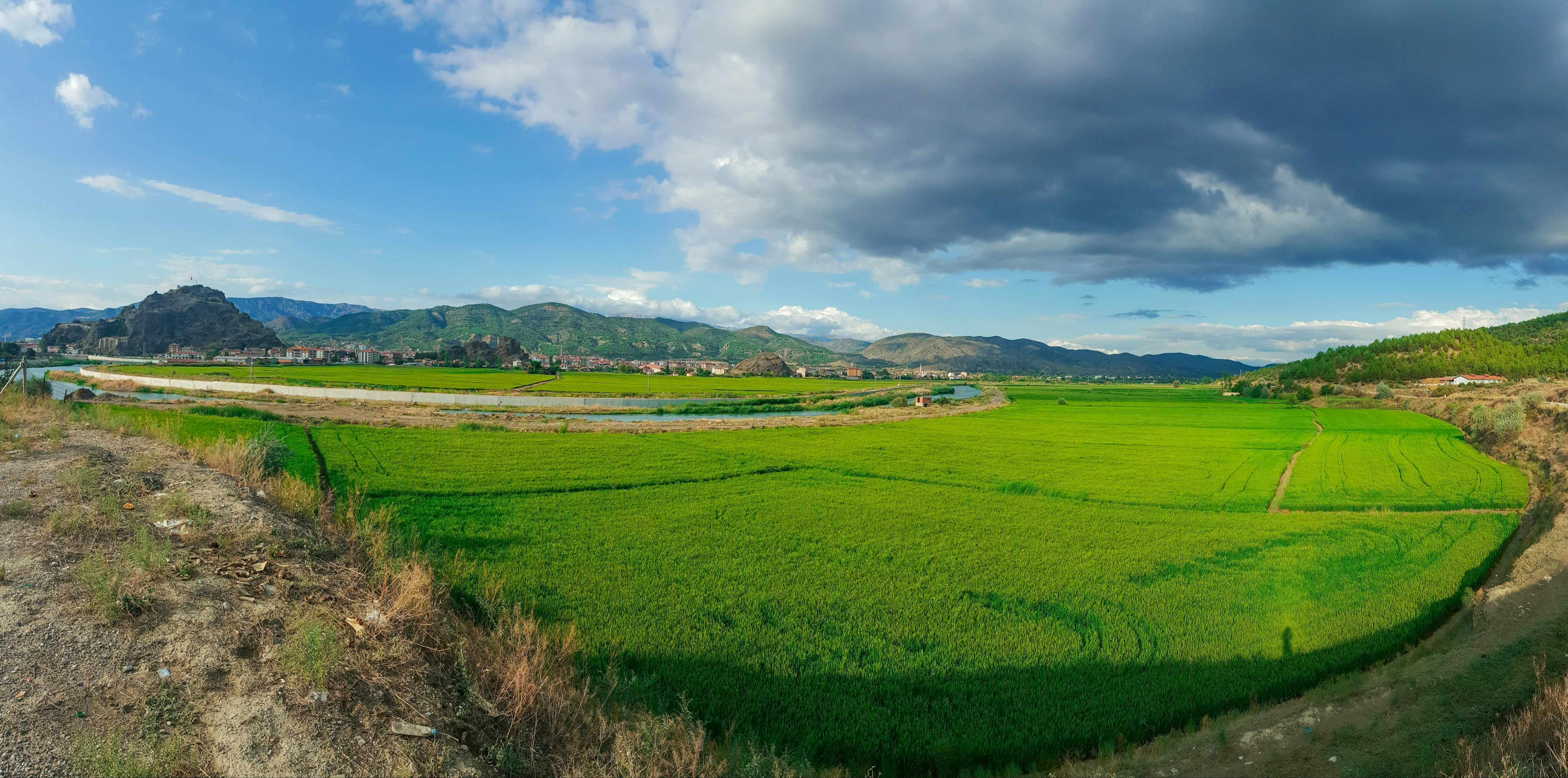 Vibrant green rice fields stretch across the valley, framed by distant mountains under a dynamic sky. The scene captures the essence of rural tranquility.