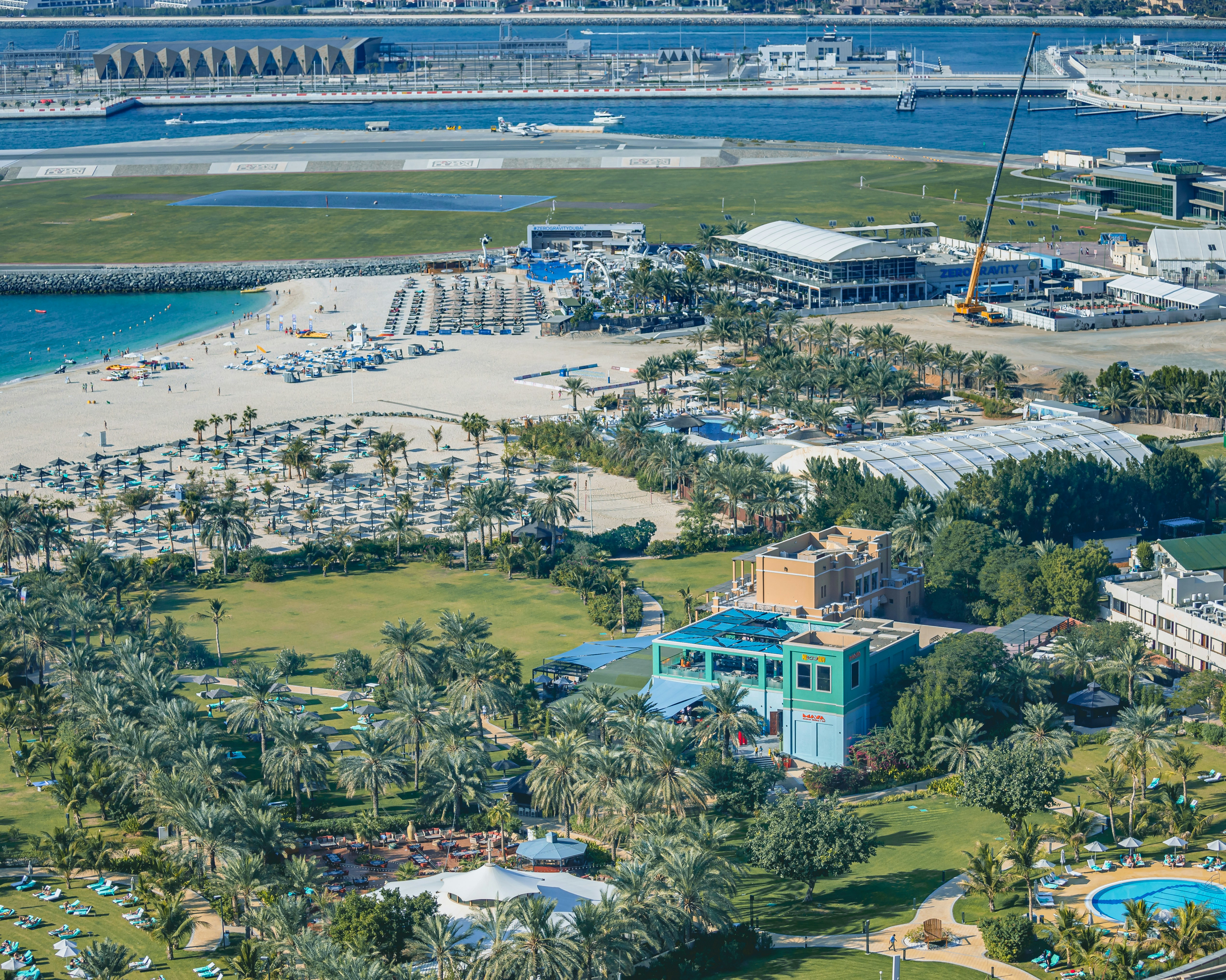 Aerial view of a vibrant beach resort, showcasing palm trees, sun loungers, and a pristine coastline. The scene captures the essence of relaxation and outdoor enjoyment.