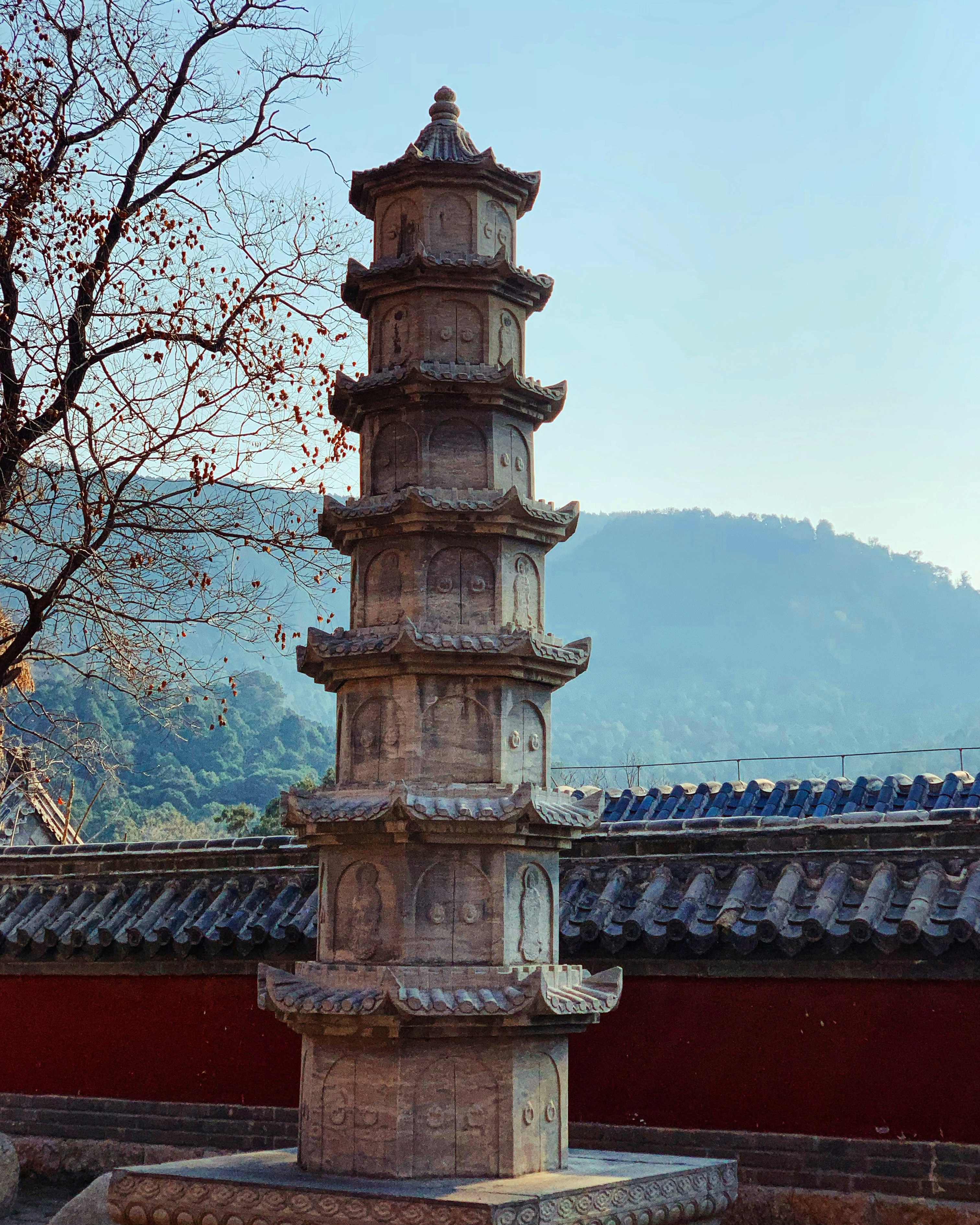 Intricate stone pagoda stands amidst a serene landscape, framed by a backdrop of distant mountains and clear blue skies.