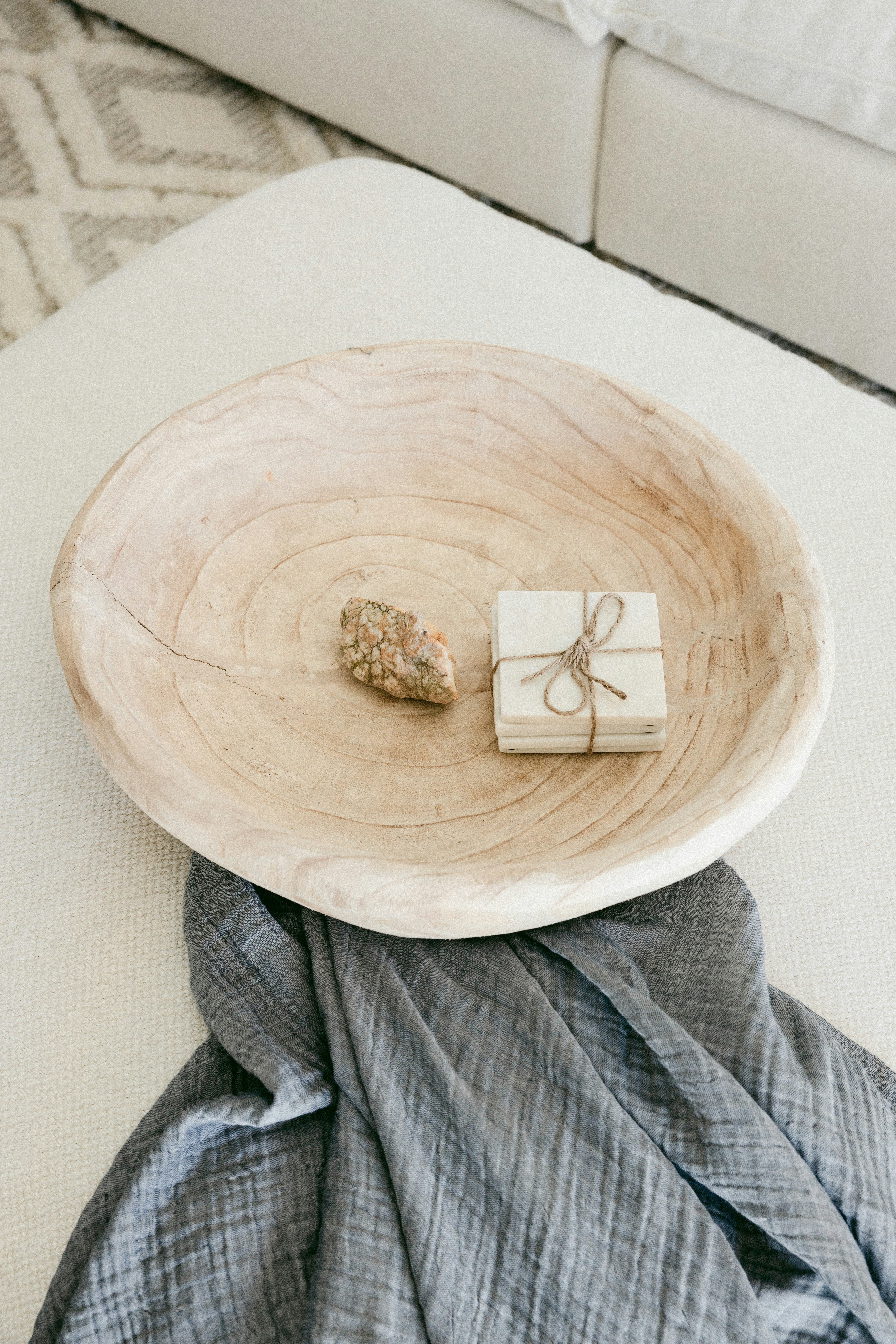 A wooden bowl containing a stone and neatly tied packages, draped with a soft gray fabric, creating a serene and minimalist arrangement.