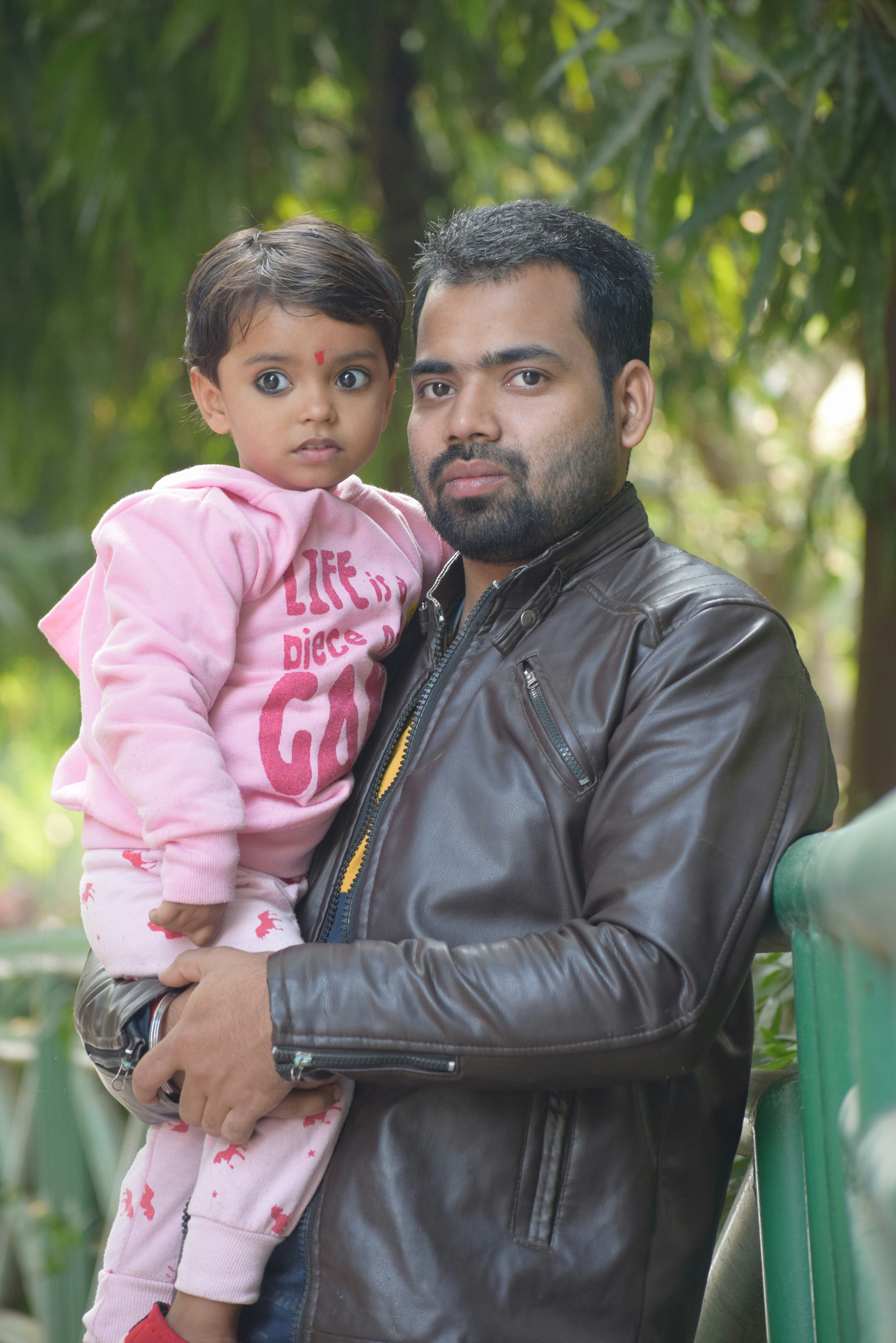 Father holding a child against a backdrop of lush greenery, capturing a moment of connection and warmth.