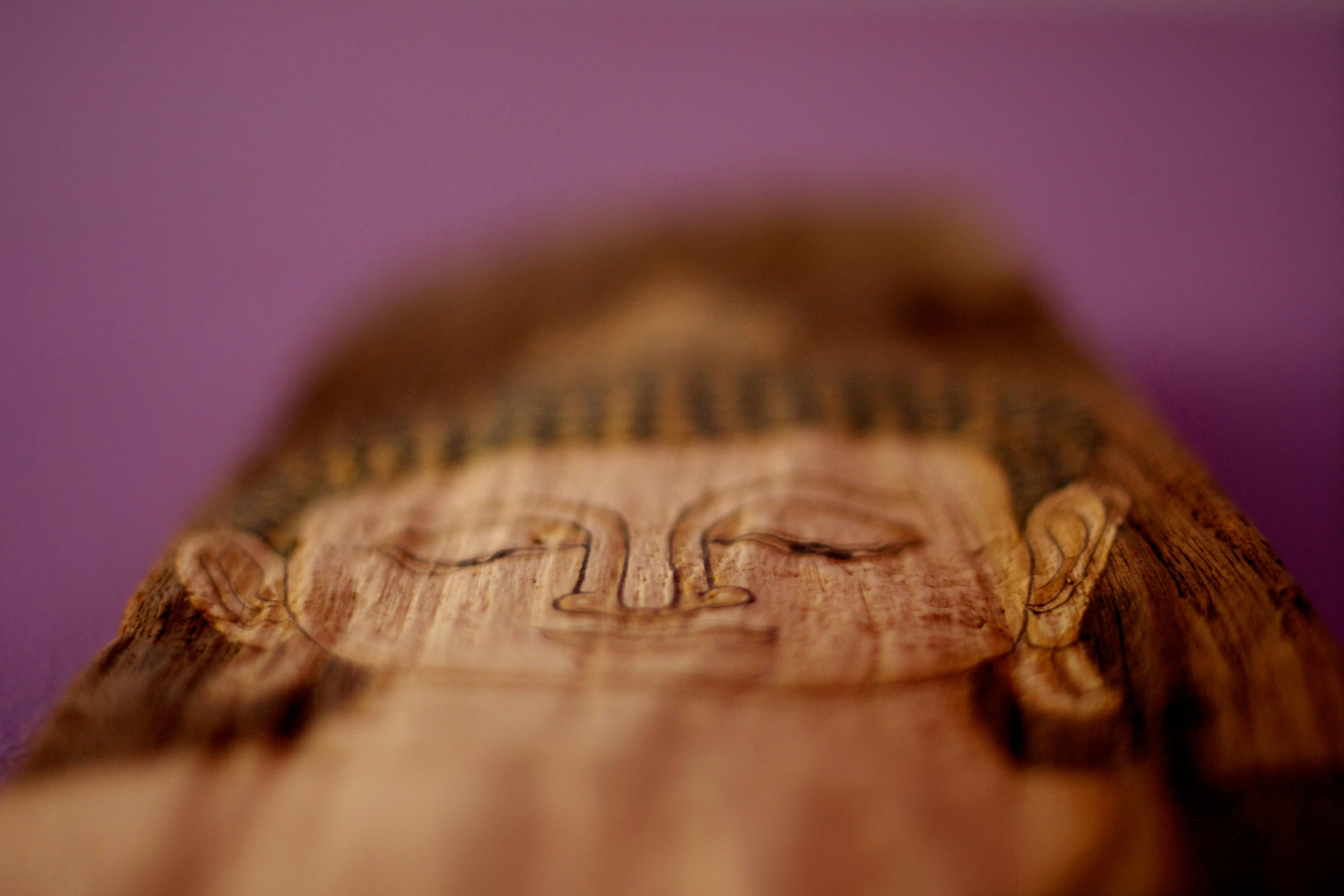 Gaze in the Grain: A Close-Up of a Carved Wooden Face in Purple Light