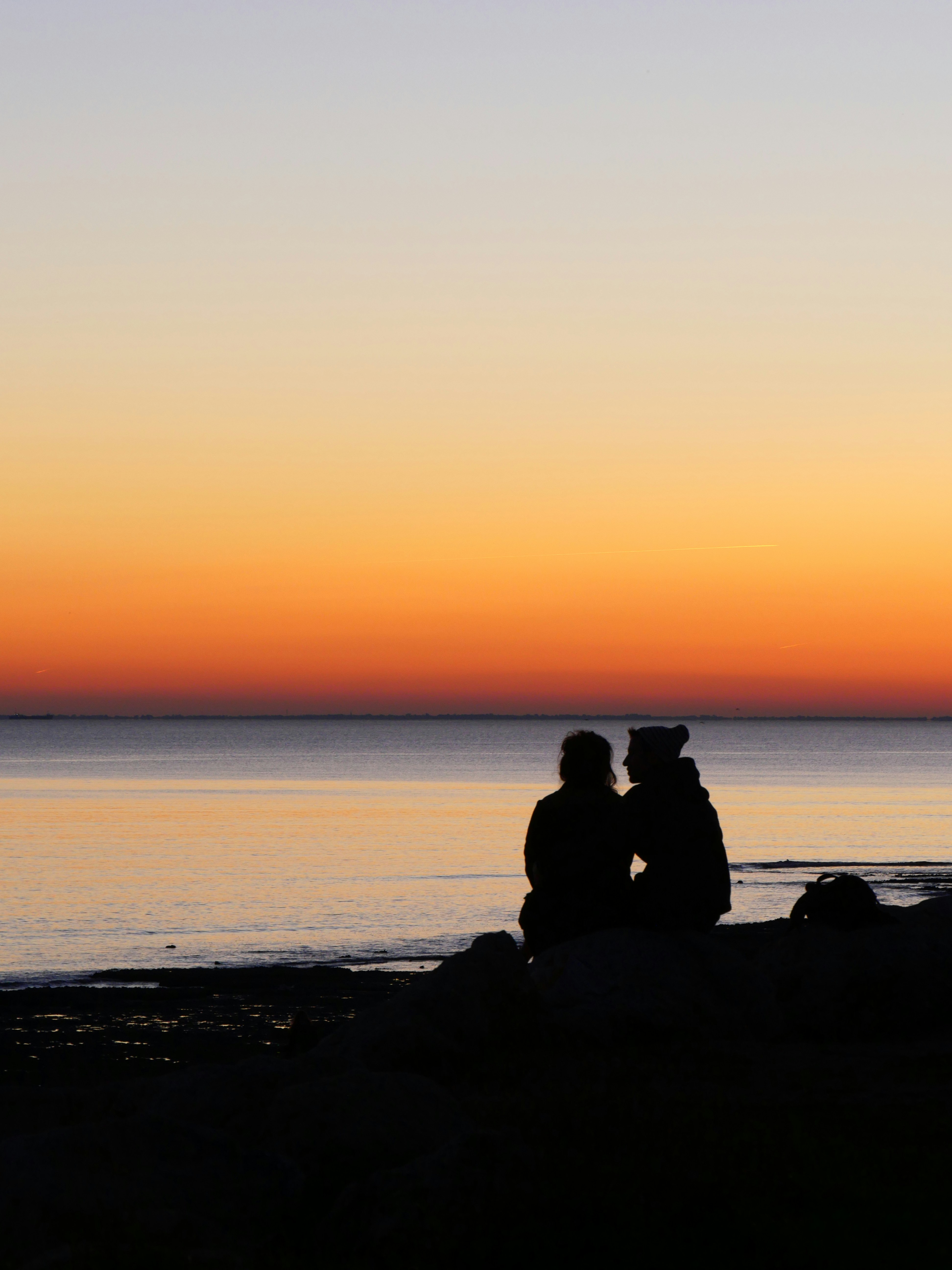 Silhouette of 2 people sitting on rock near sea during sunset photo ...