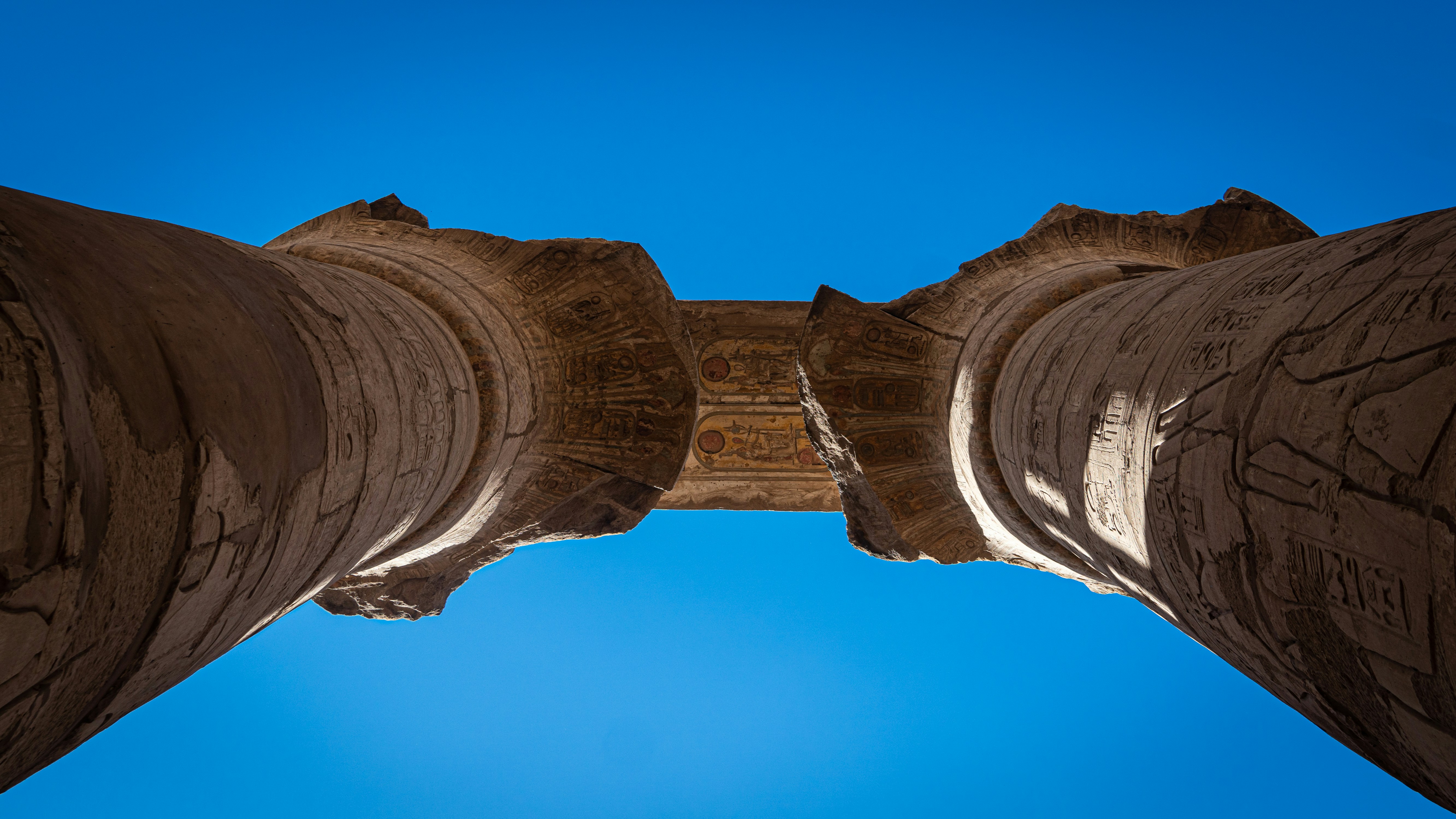 View from below two towering ancient columns with a decorative archway against a clear blue sky.