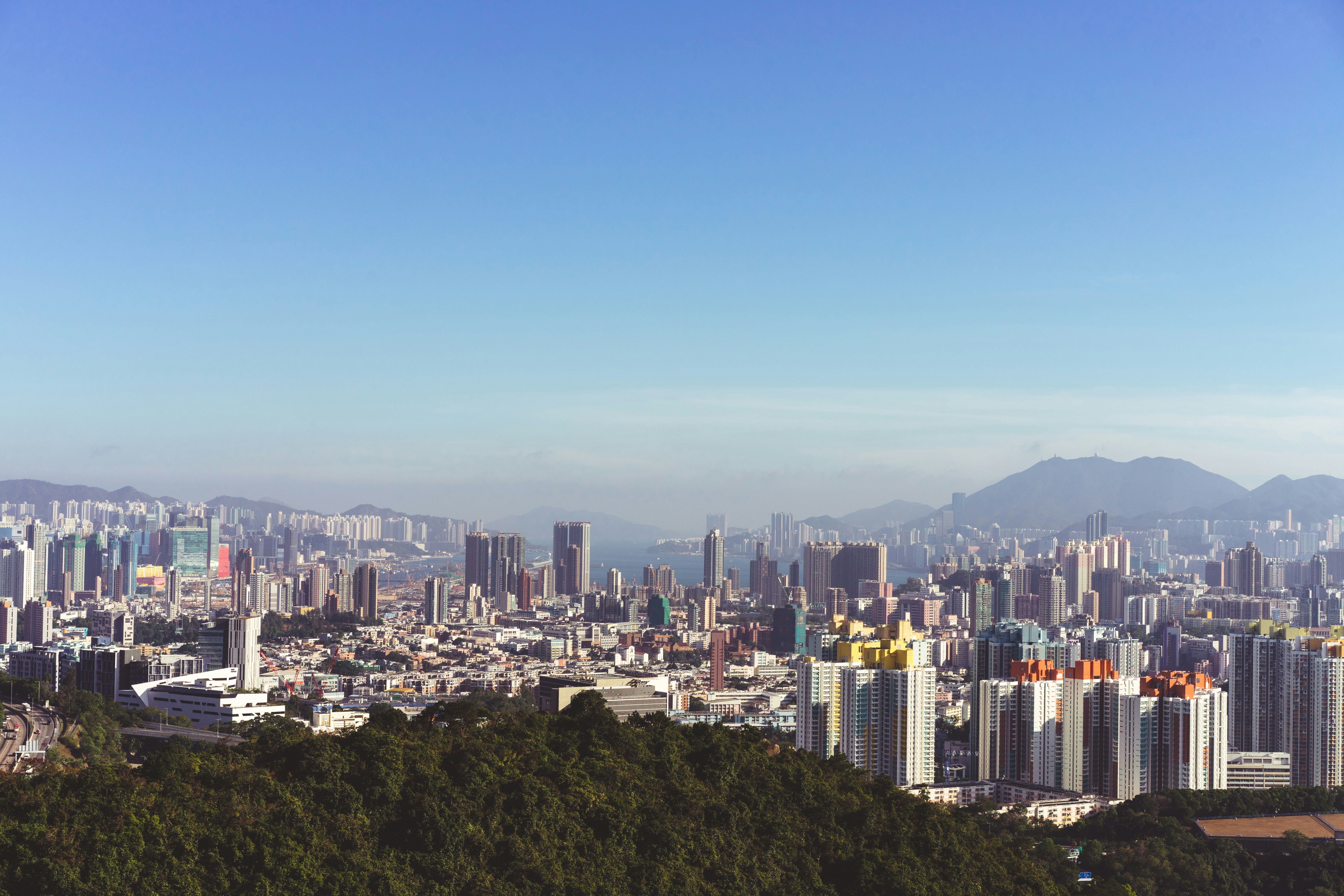 Vast cityscape showcasing a blend of modern skyscrapers and lush greenery, with distant mountains framing the horizon.