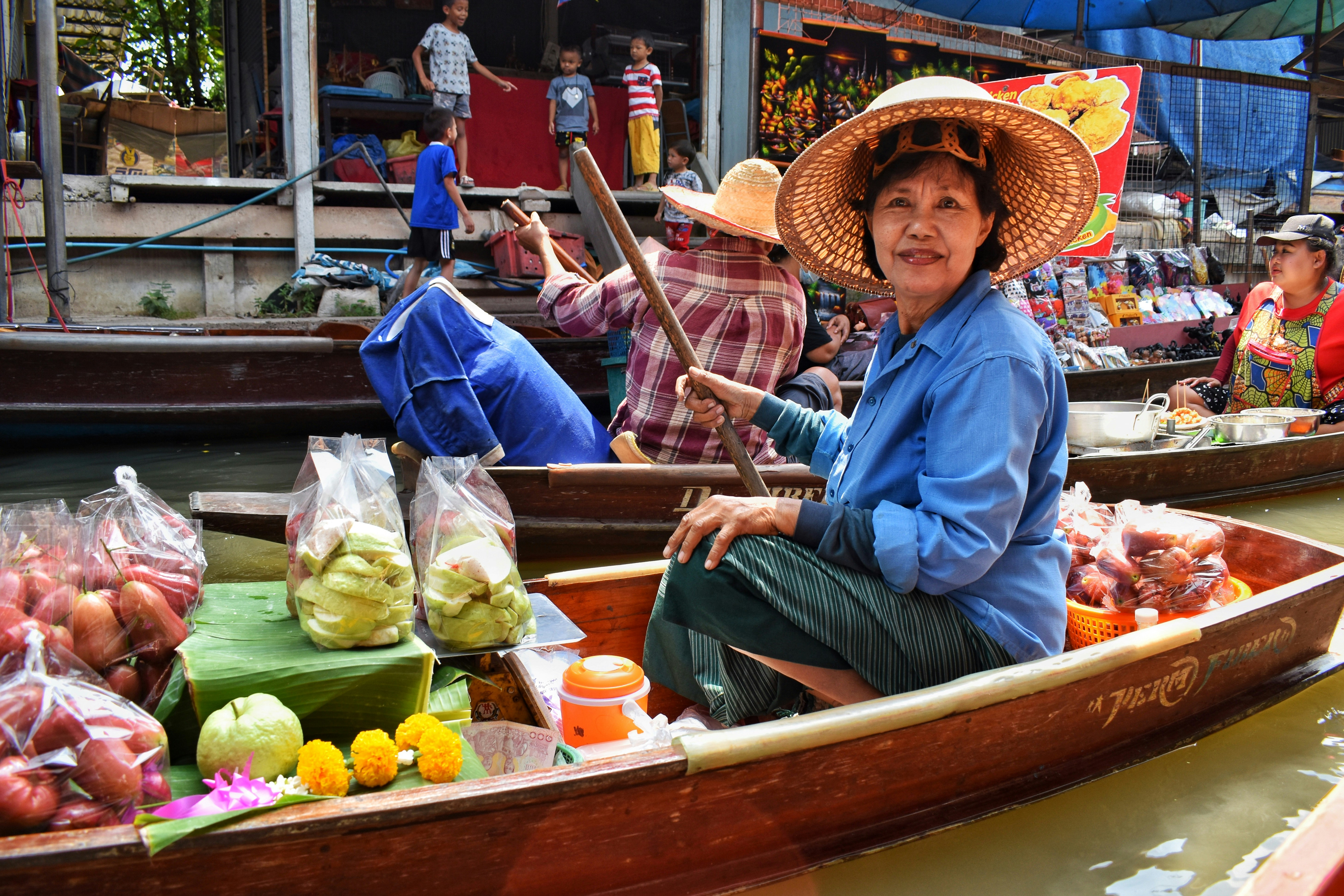 A vendor in a traditional boat selling fresh fruits at a bustling floating market, surrounded by vibrant displays of produce. The scene captures the essence of local commerce and community interaction.