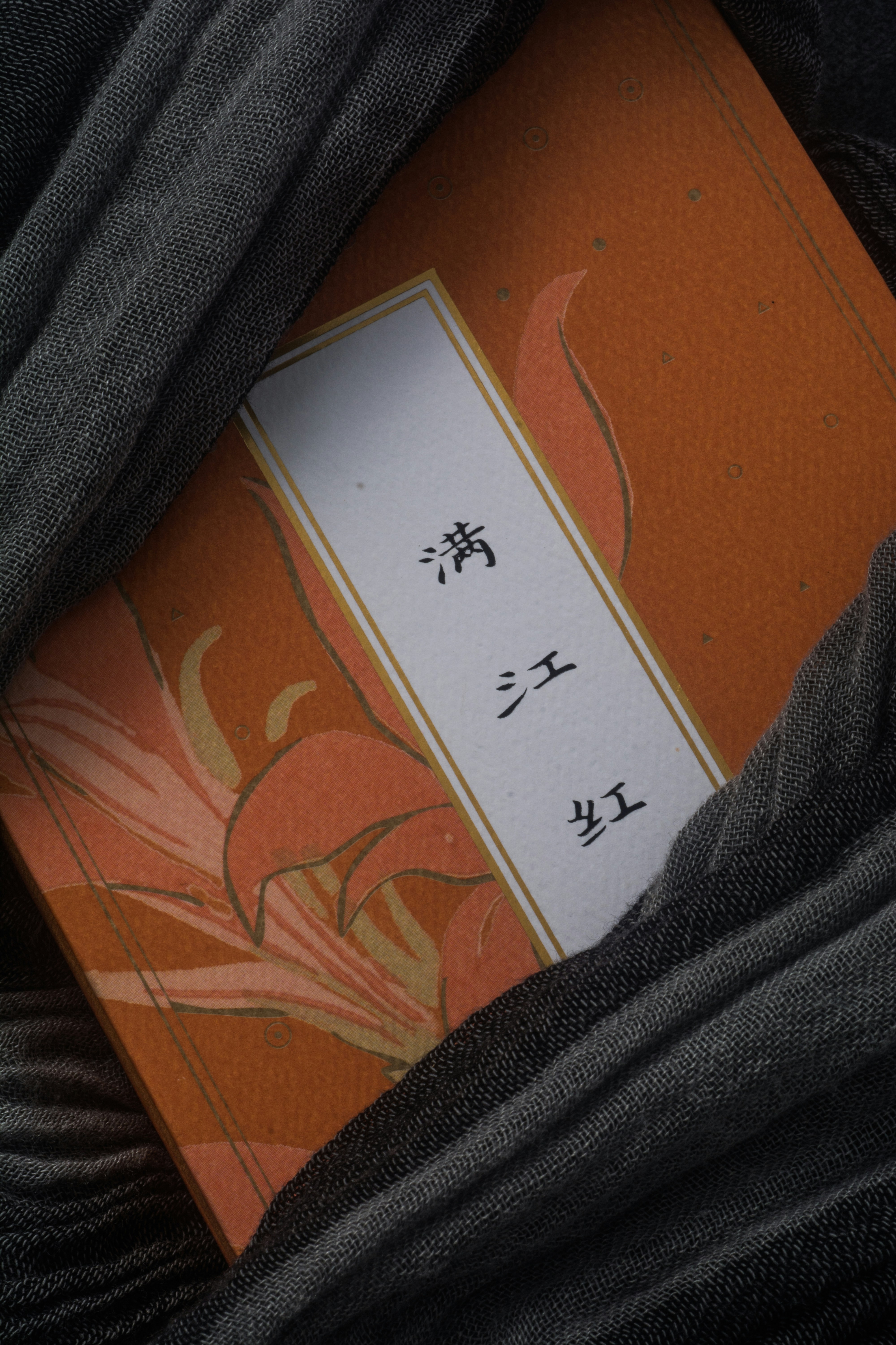 An intricately designed book cover partially obscured by flowing fabric, showcasing elegant floral motifs and Chinese characters.