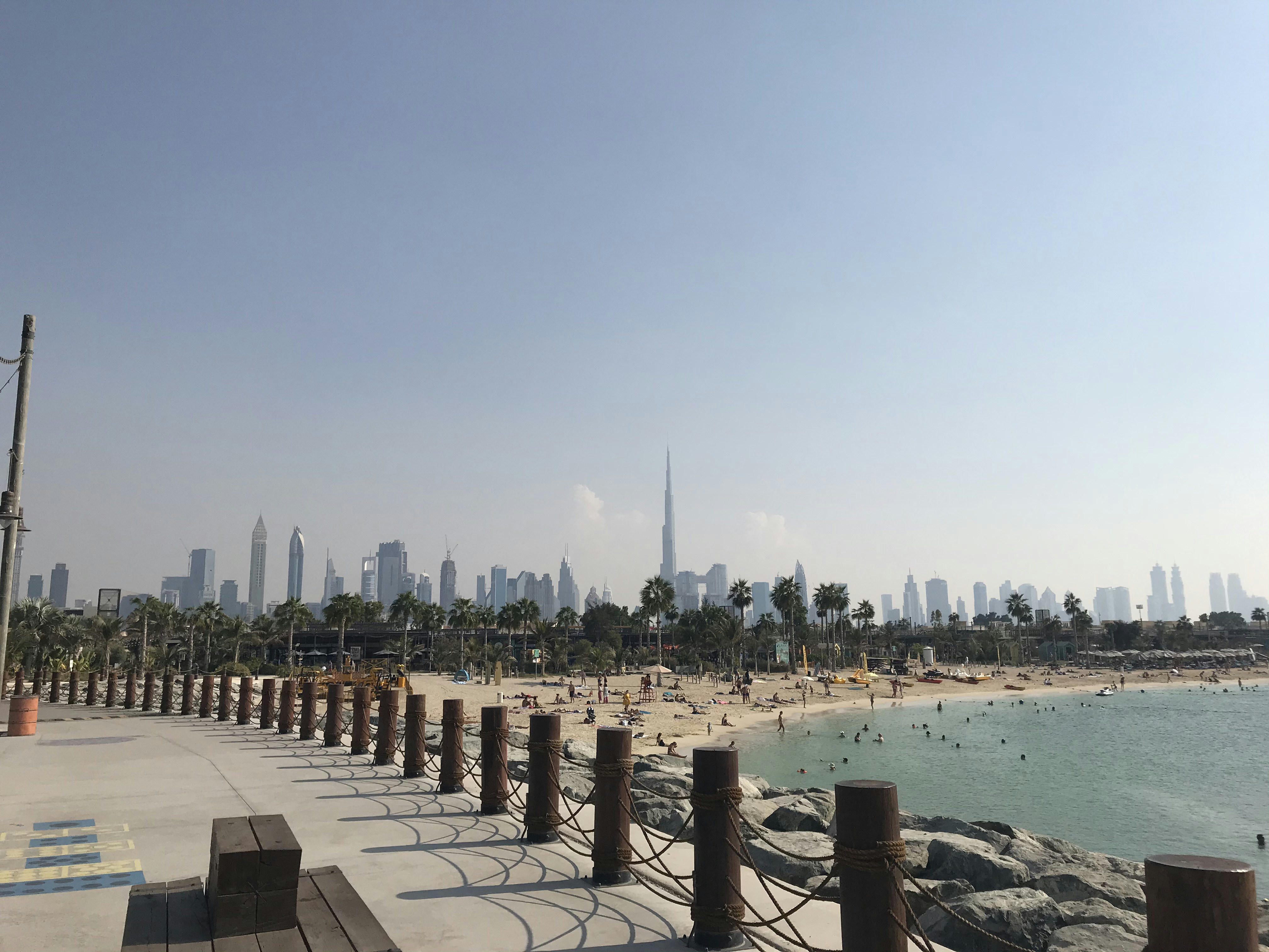 Urban skyline with iconic skyscraper viewed from a sunny beach promenade.