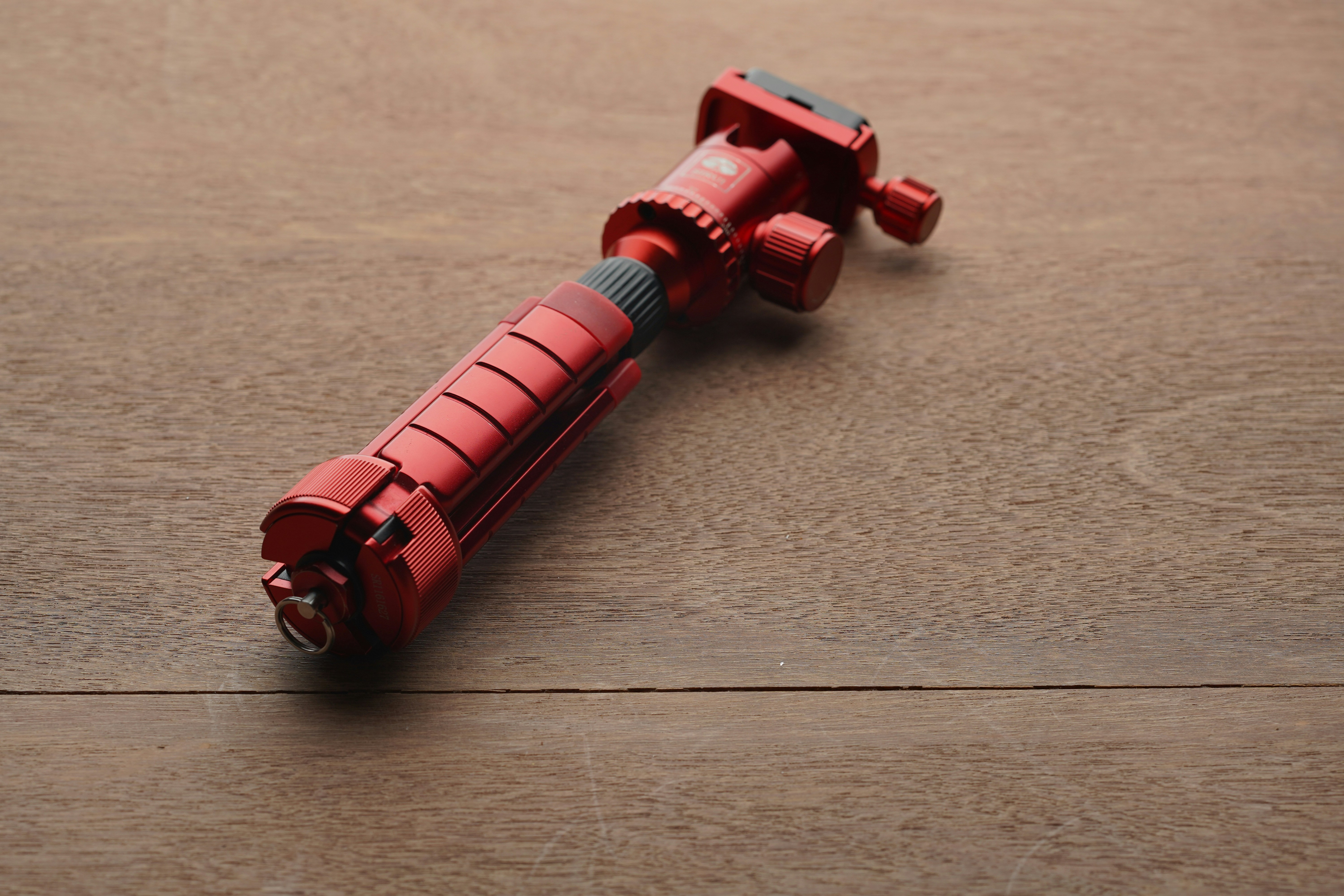 Mini tripod folded on a wooden table | red and black plastic toy