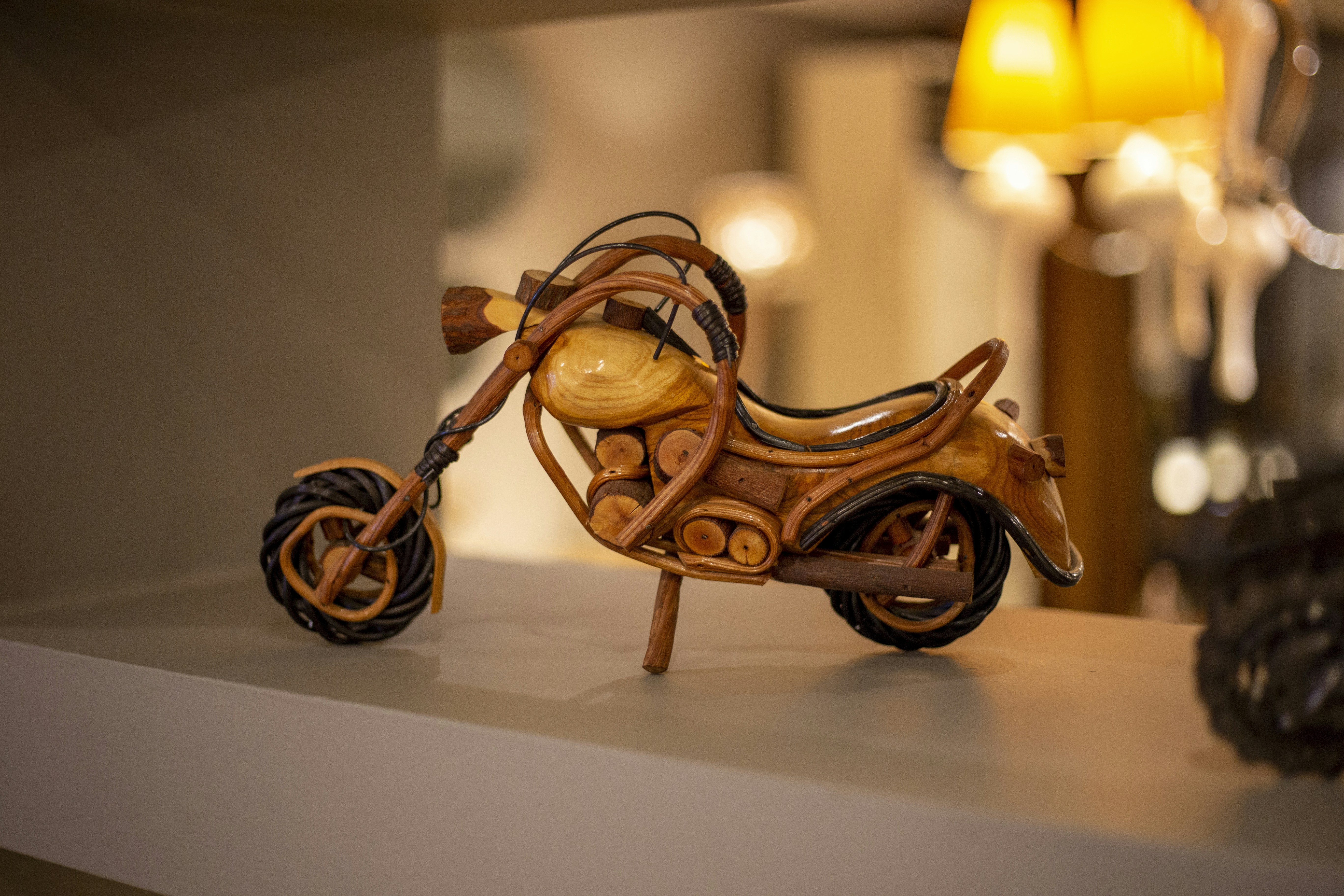 Amber-lit wooden motorcycle sculpture on a calm white shelf