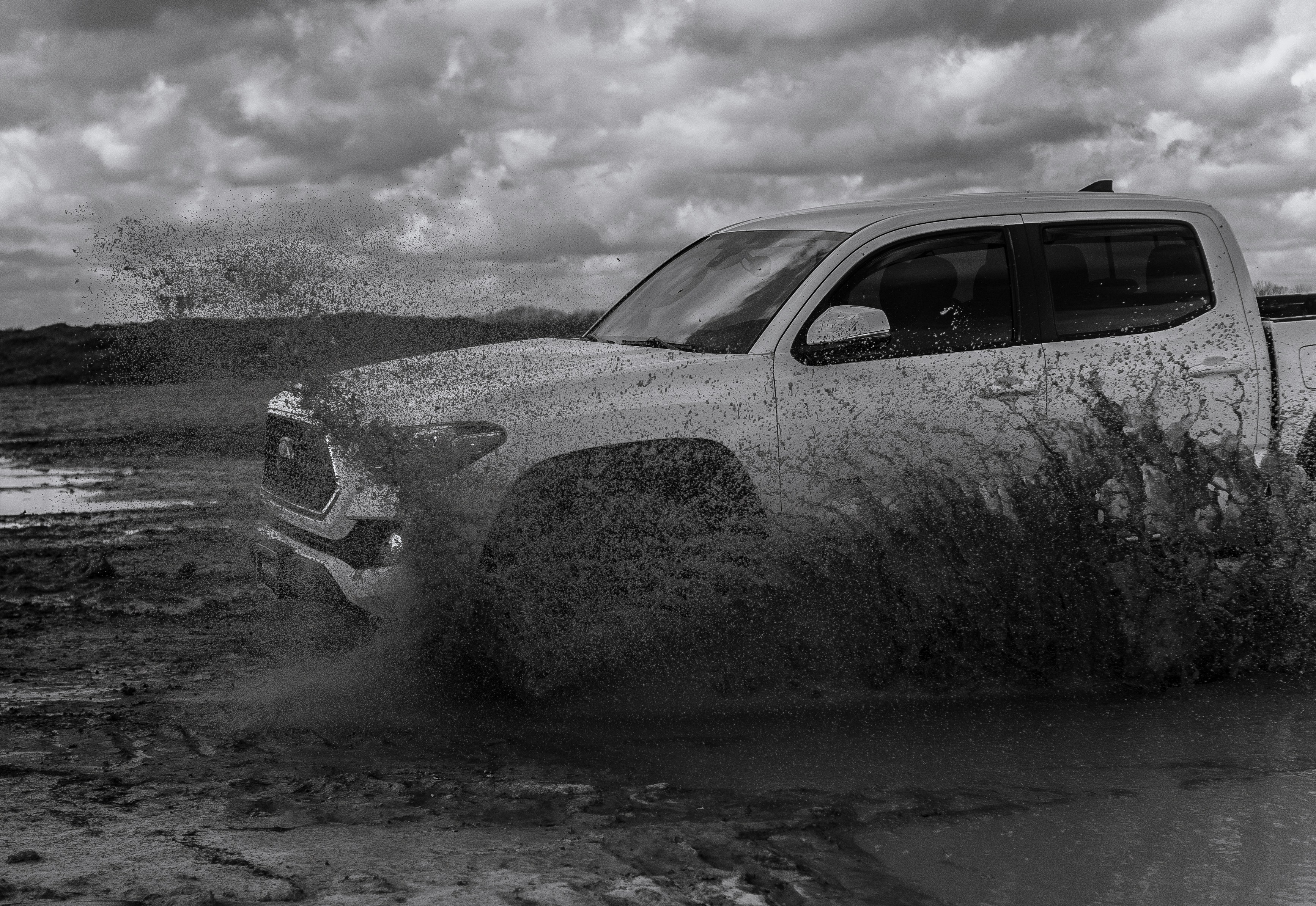 Pickup truck navigating through a muddy terrain under a cloudy sky.