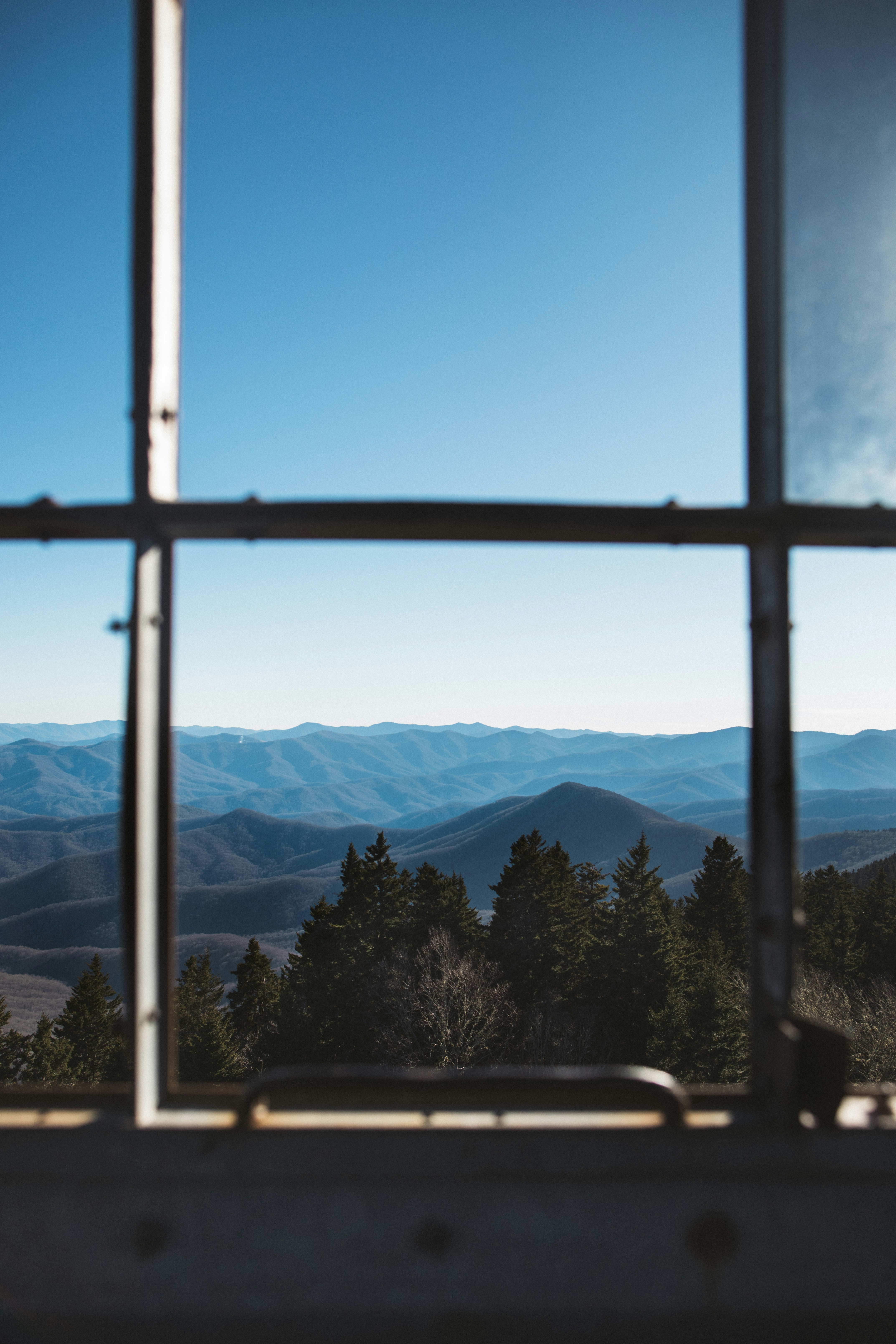Mountain landscape viewed through a rustic window frame, showcasing layers of hills under a clear blue sky.