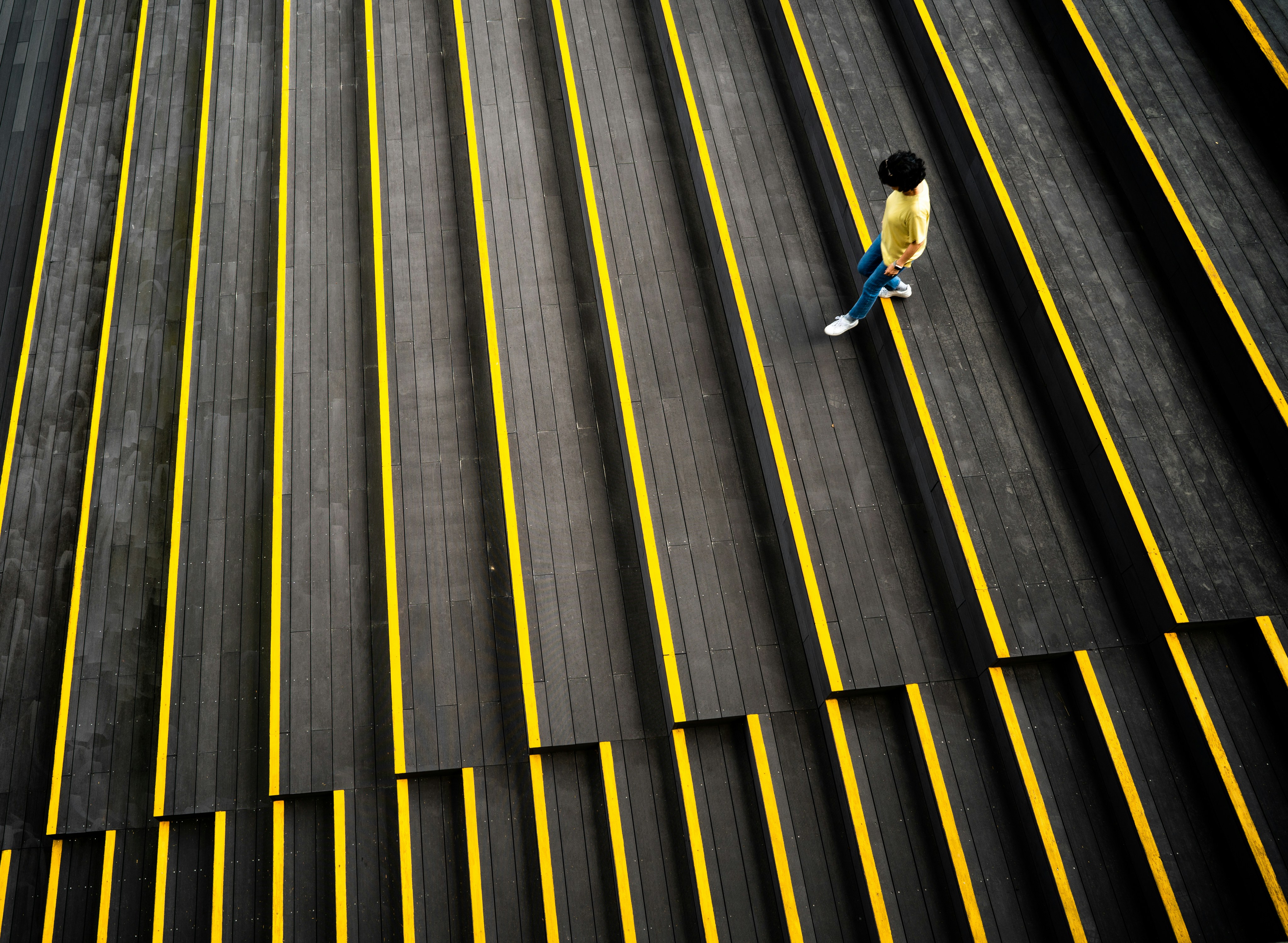 Individual walking along a series of wooden steps highlighted by vibrant yellow lines, creating a striking visual contrast and sense of movement.