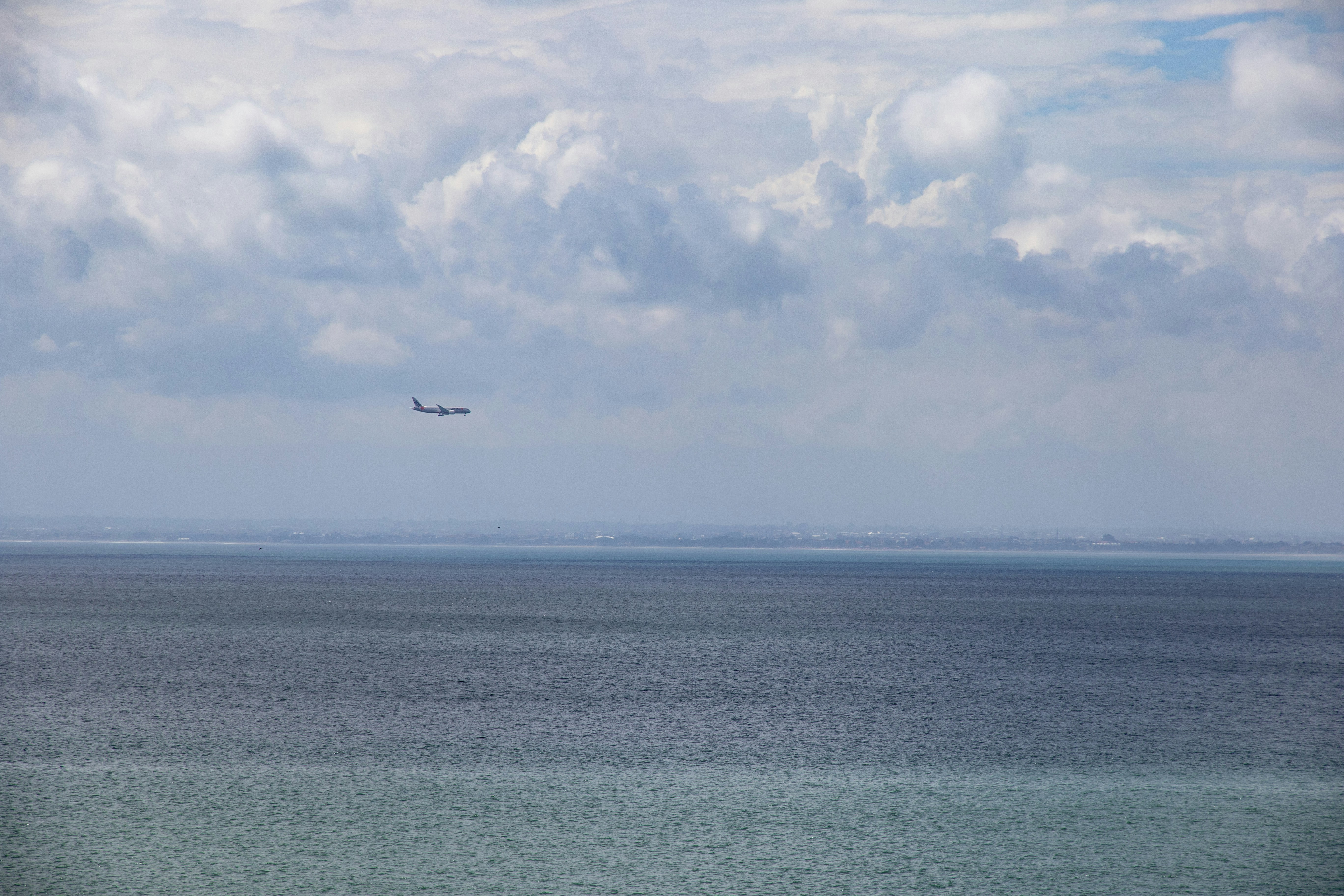 Airplane soaring above a vast ocean under a sky filled with dramatic clouds.