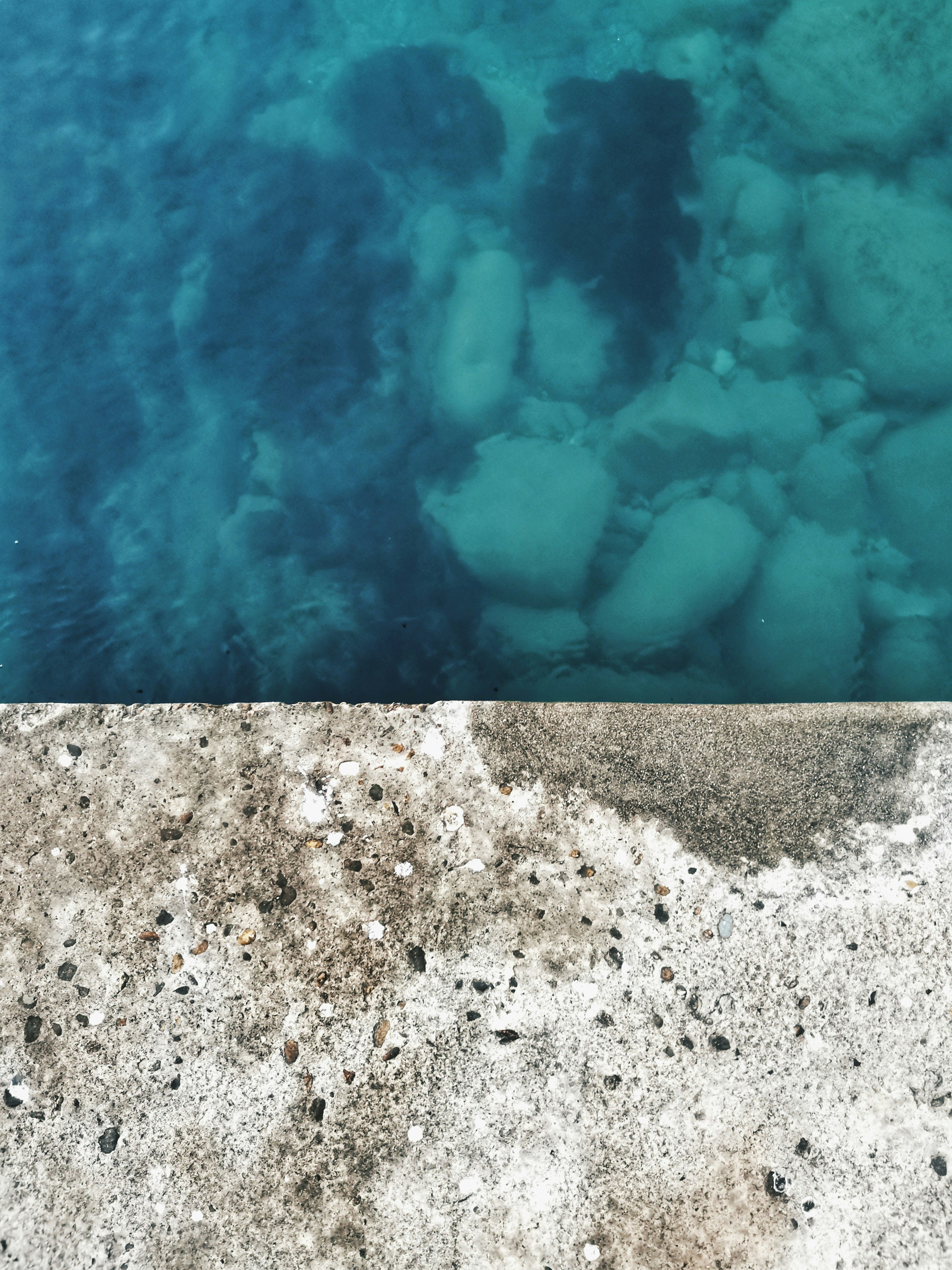 Turquoise water pools along a weathered concrete edge, with submerged rocks visible beneath the surface.