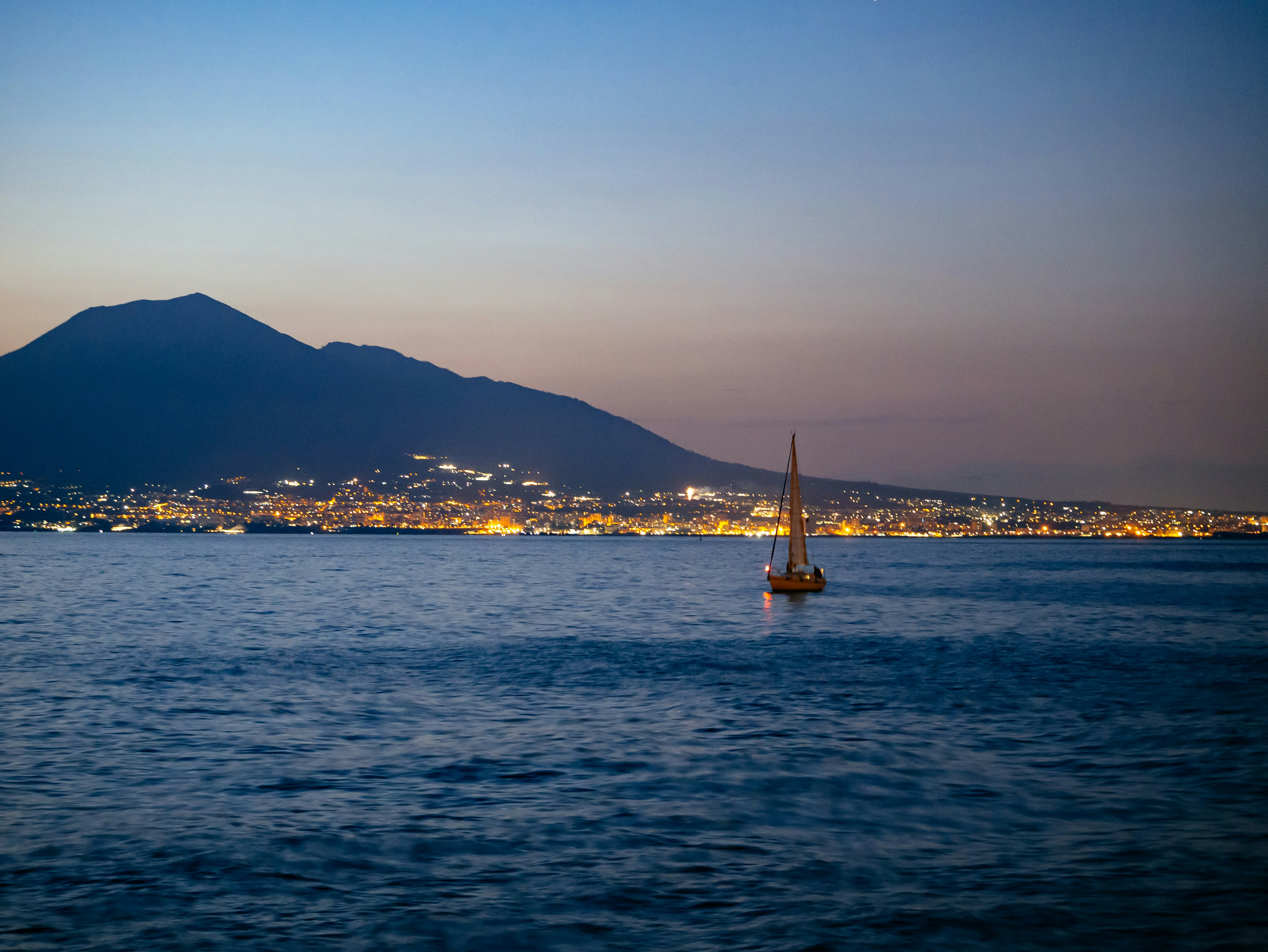 Sailboat on the Gulf of Naples with Mount Vesuvius in the background during a warm evening.