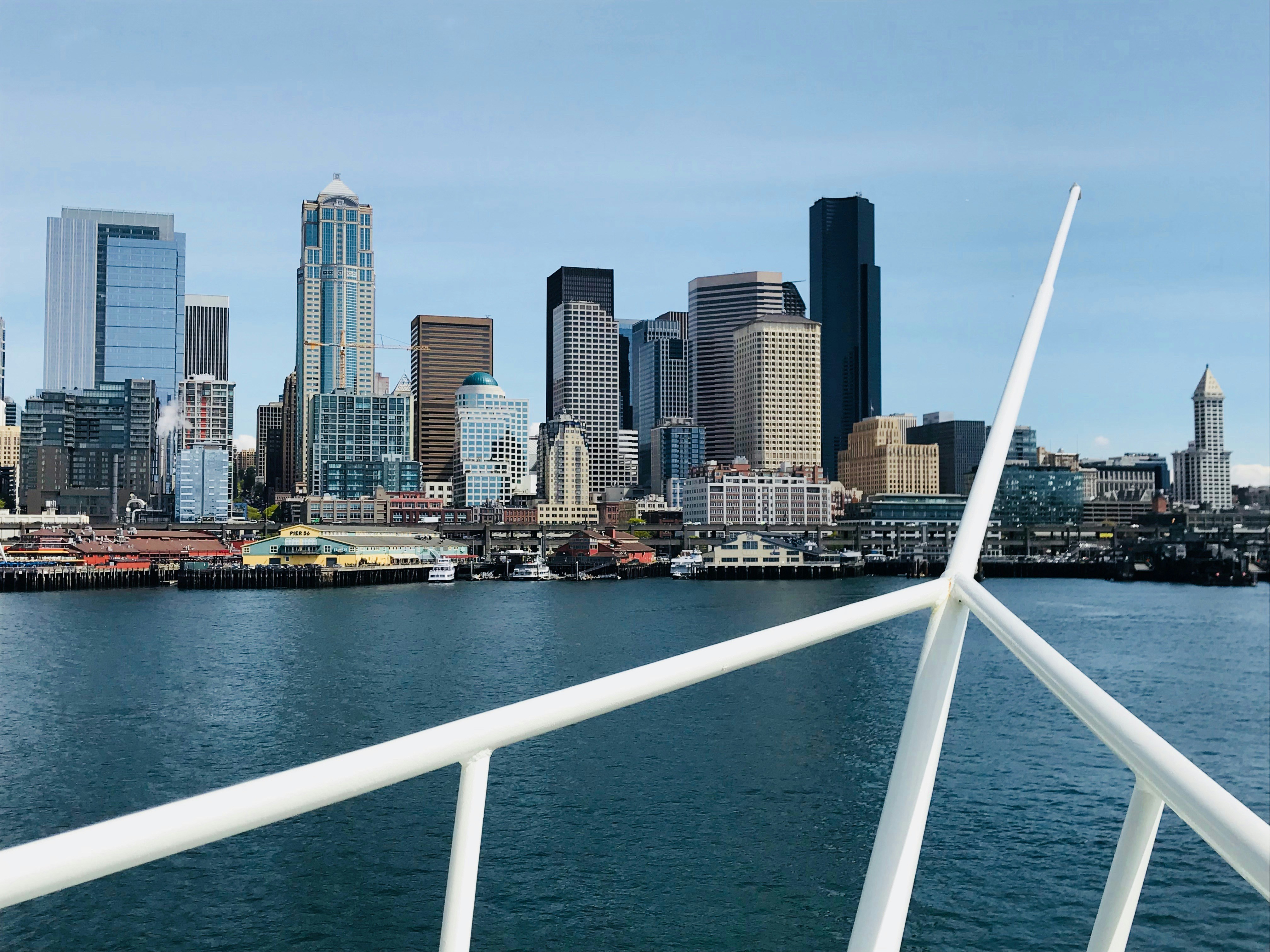 Seattle skyline viewed from ferry with foreground railing and calm waters under a clear sky.