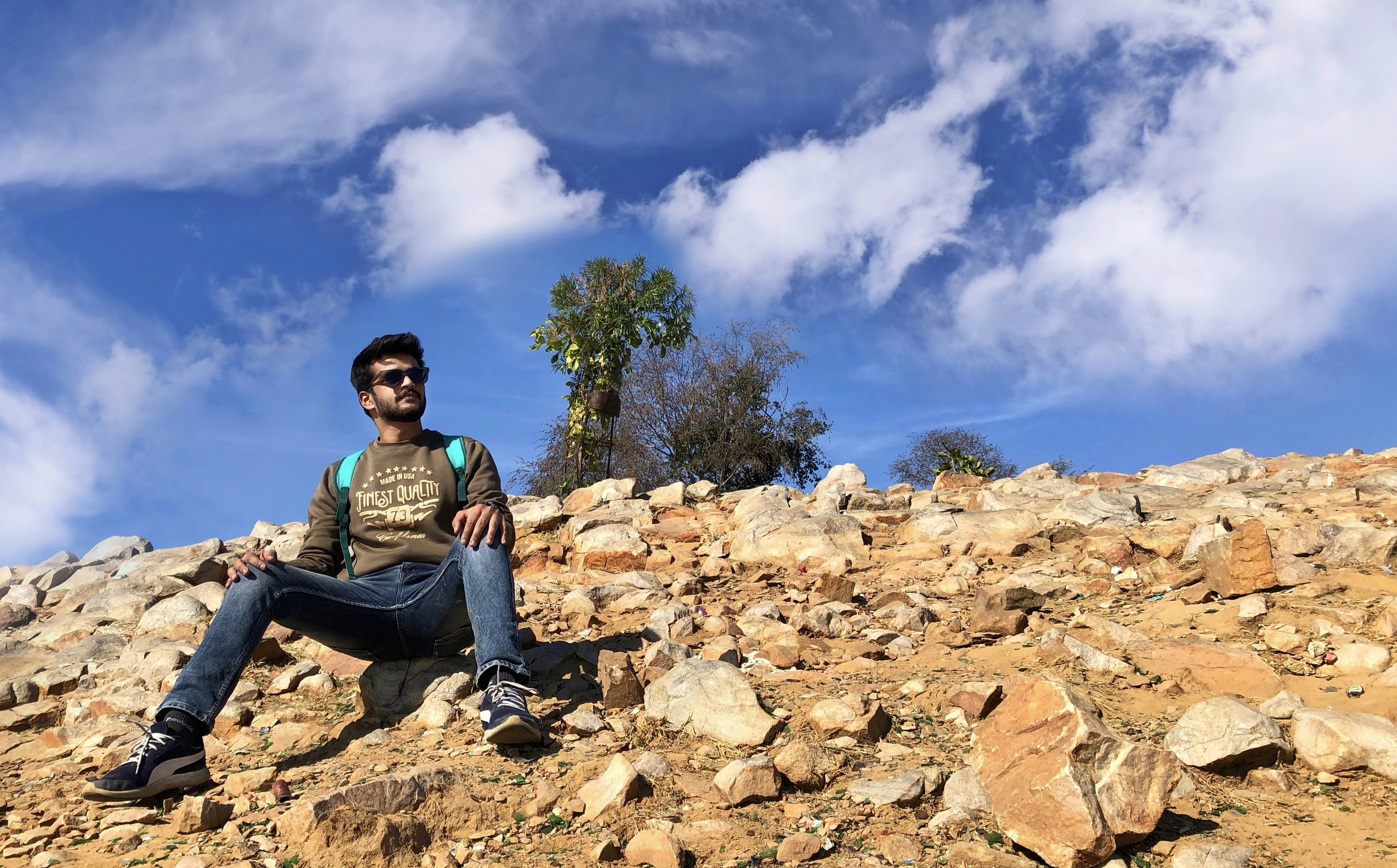 Person sitting on rocky terrain under a vibrant blue sky with scattered clouds.