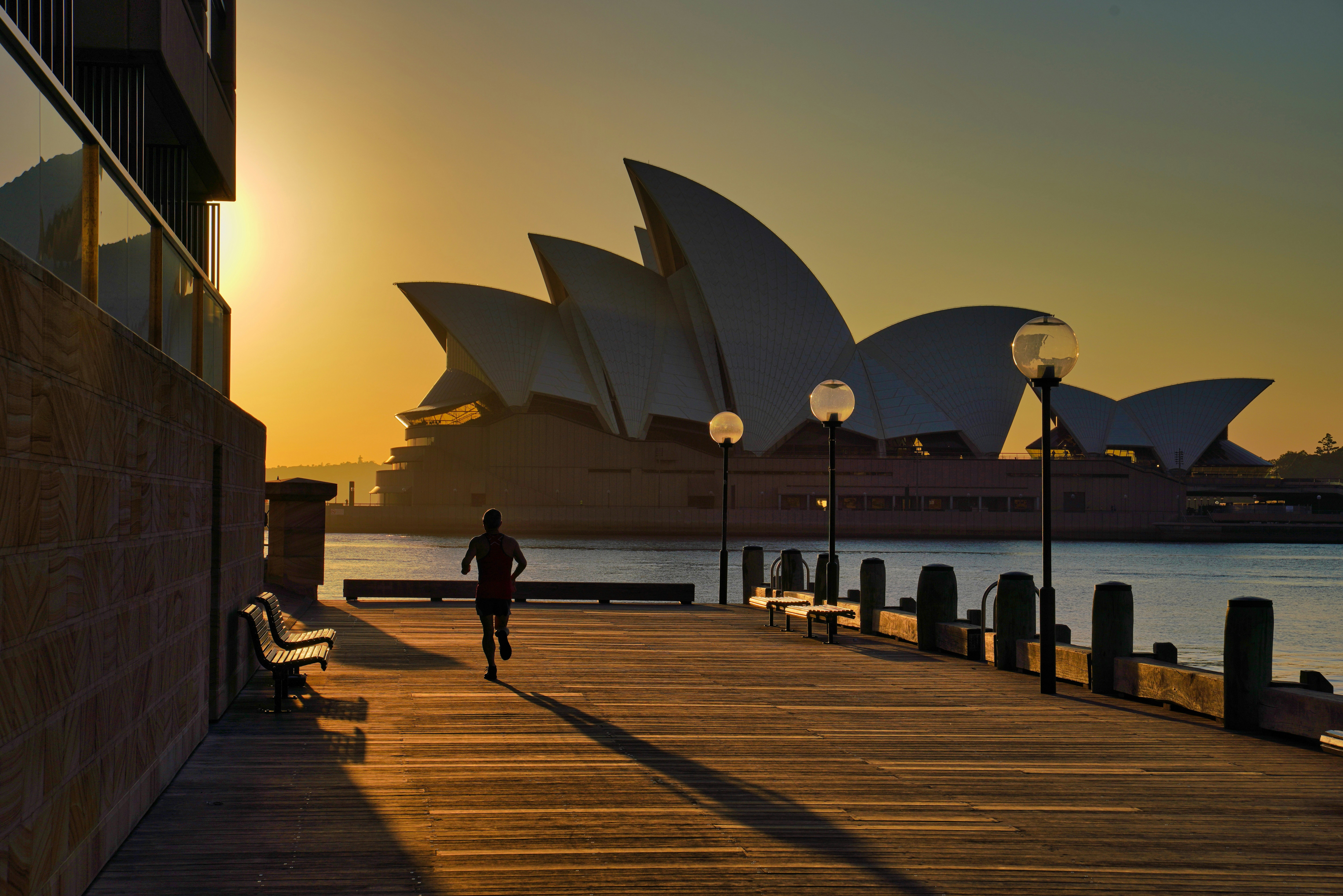 Silhouette of a person jogging on a dock with the Sydney Opera House in the background at sunrise.