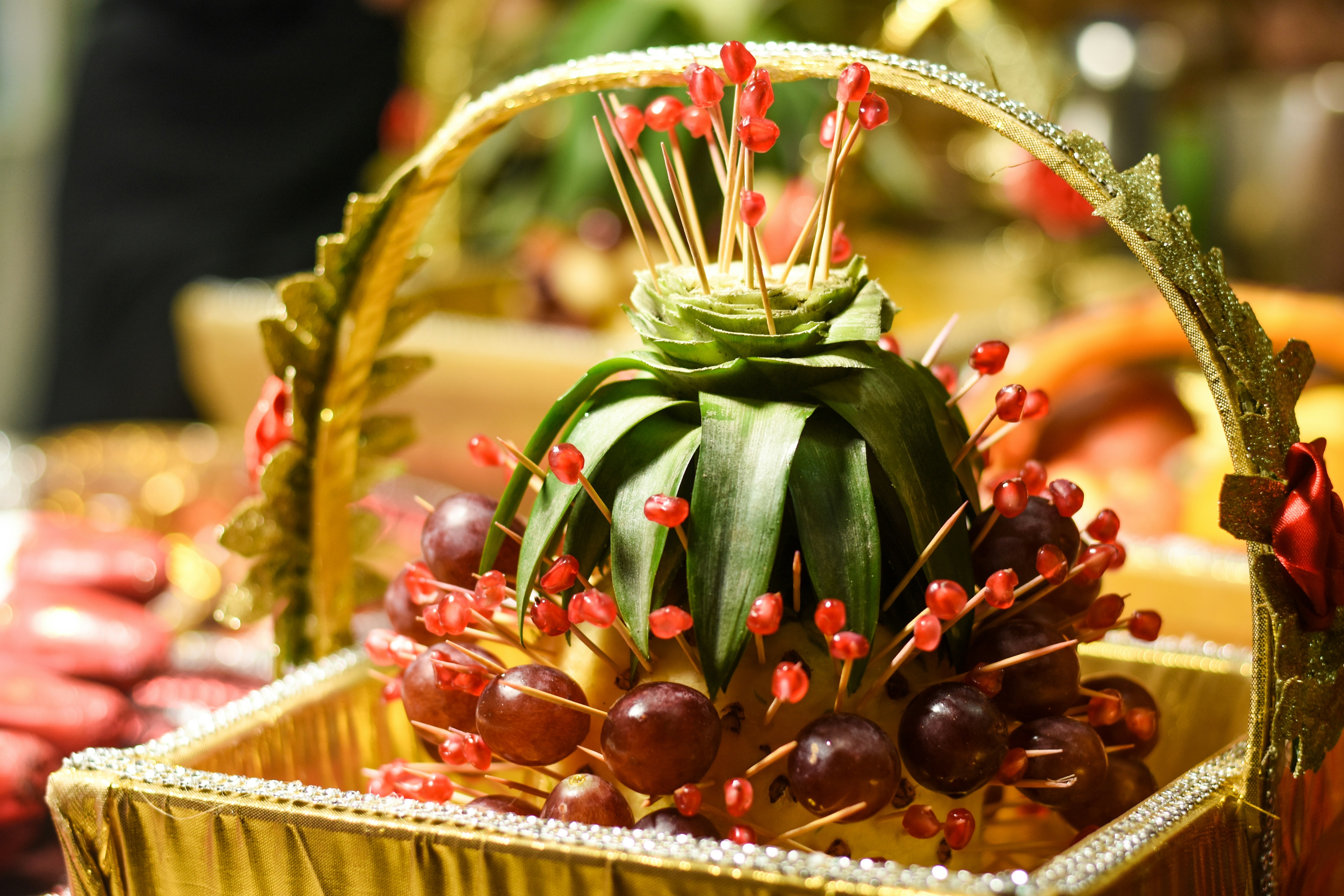 Intricately arranged fruit centerpiece featuring a pineapple base adorned with grapes and decorative skewers, set against a vibrant backdrop.