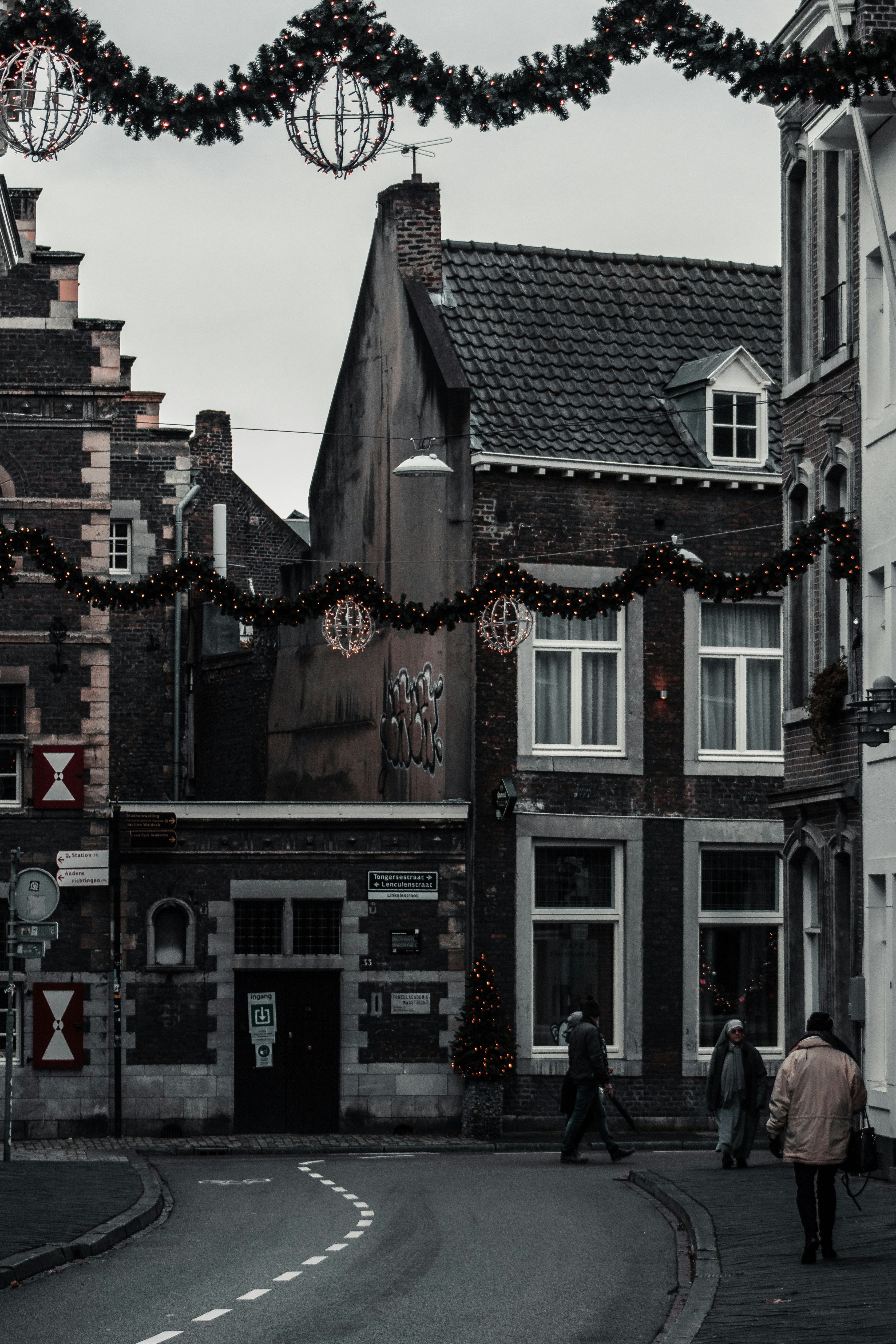 Charming urban street adorned with festive decorations, featuring historic buildings and pedestrians strolling amidst a muted winter atmosphere.