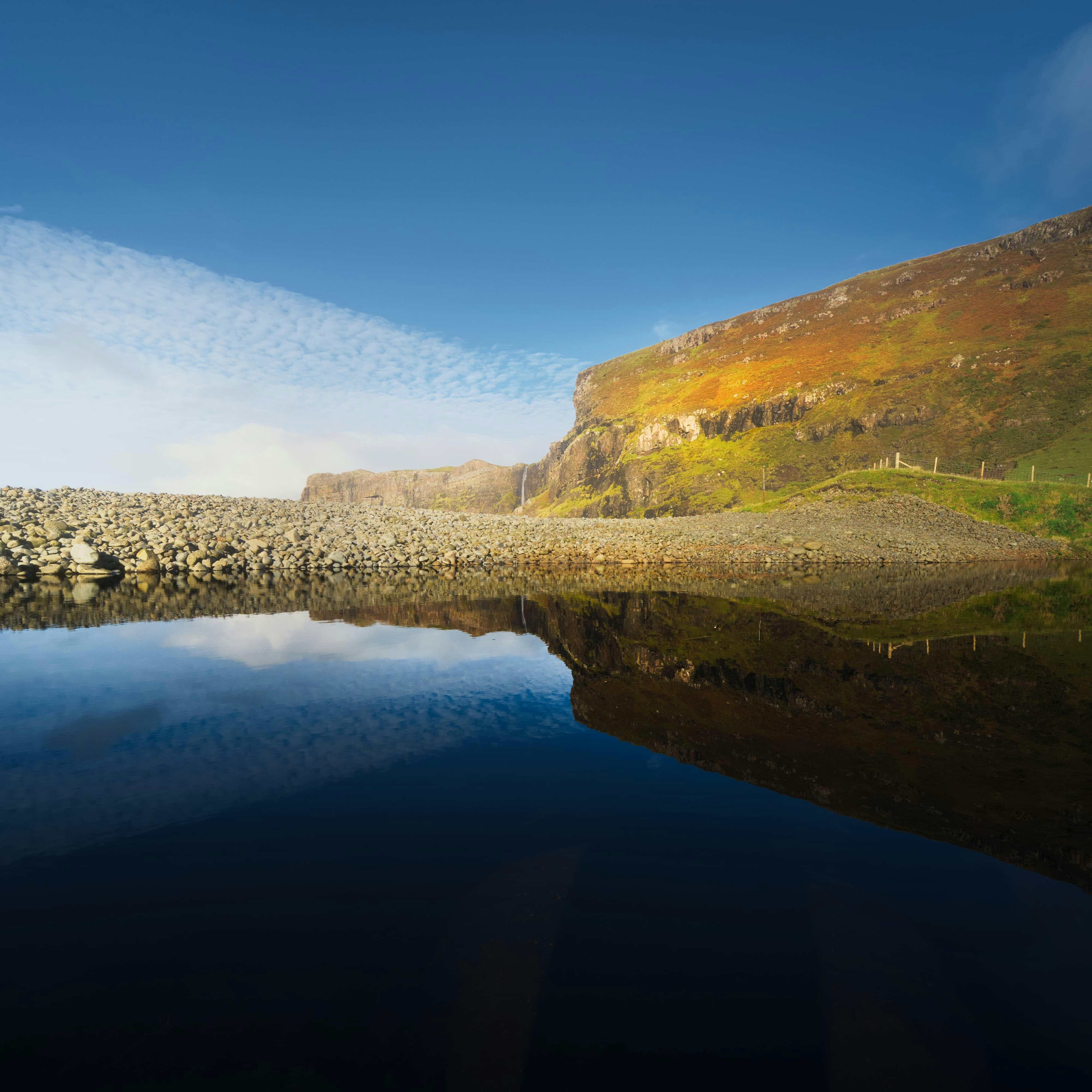 Cliffside Glow Over a Tranquil Sea, Reflected Under a Pristine Sky