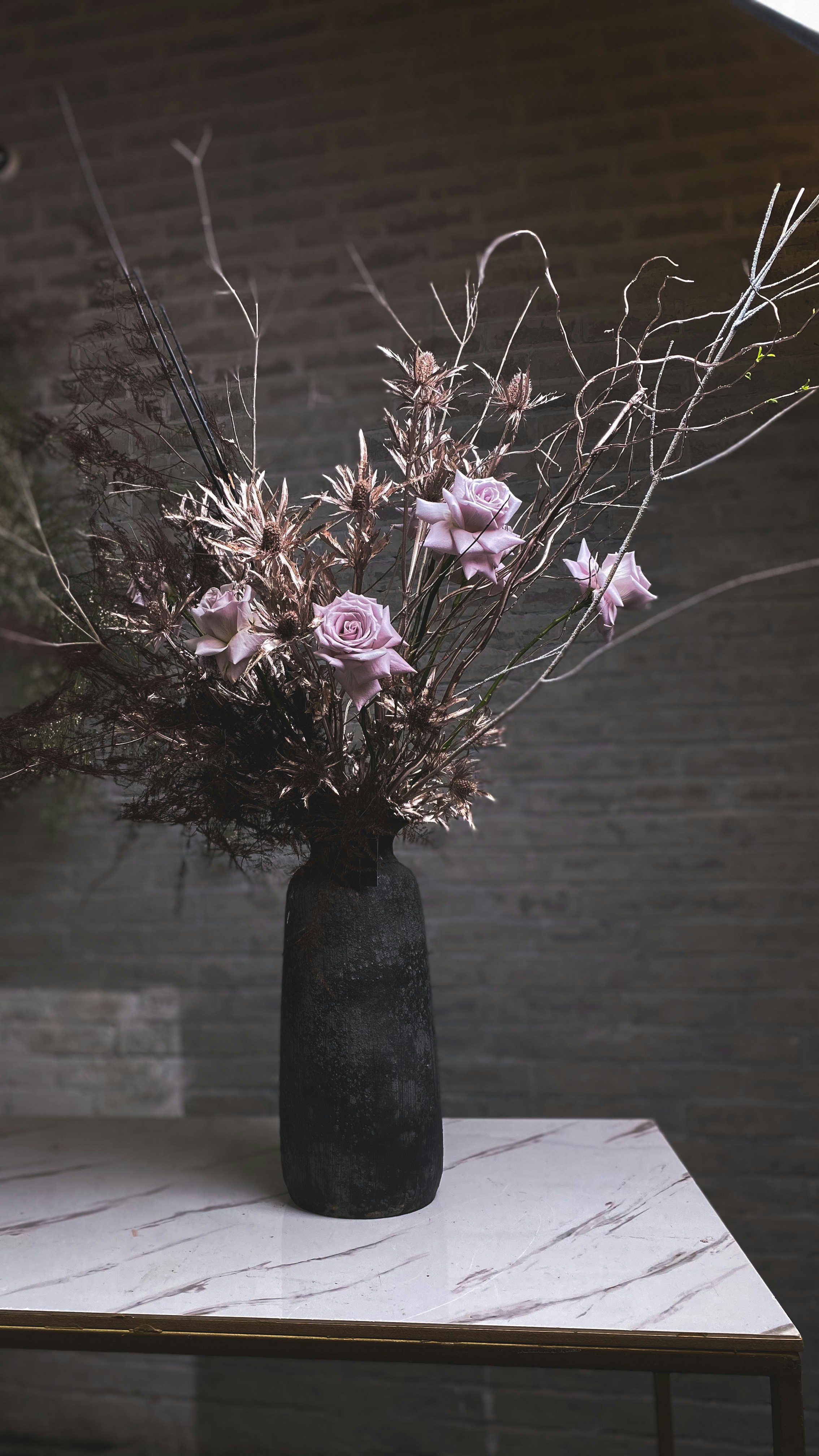 Vase of muted pink roses and dried stems on a marble table
