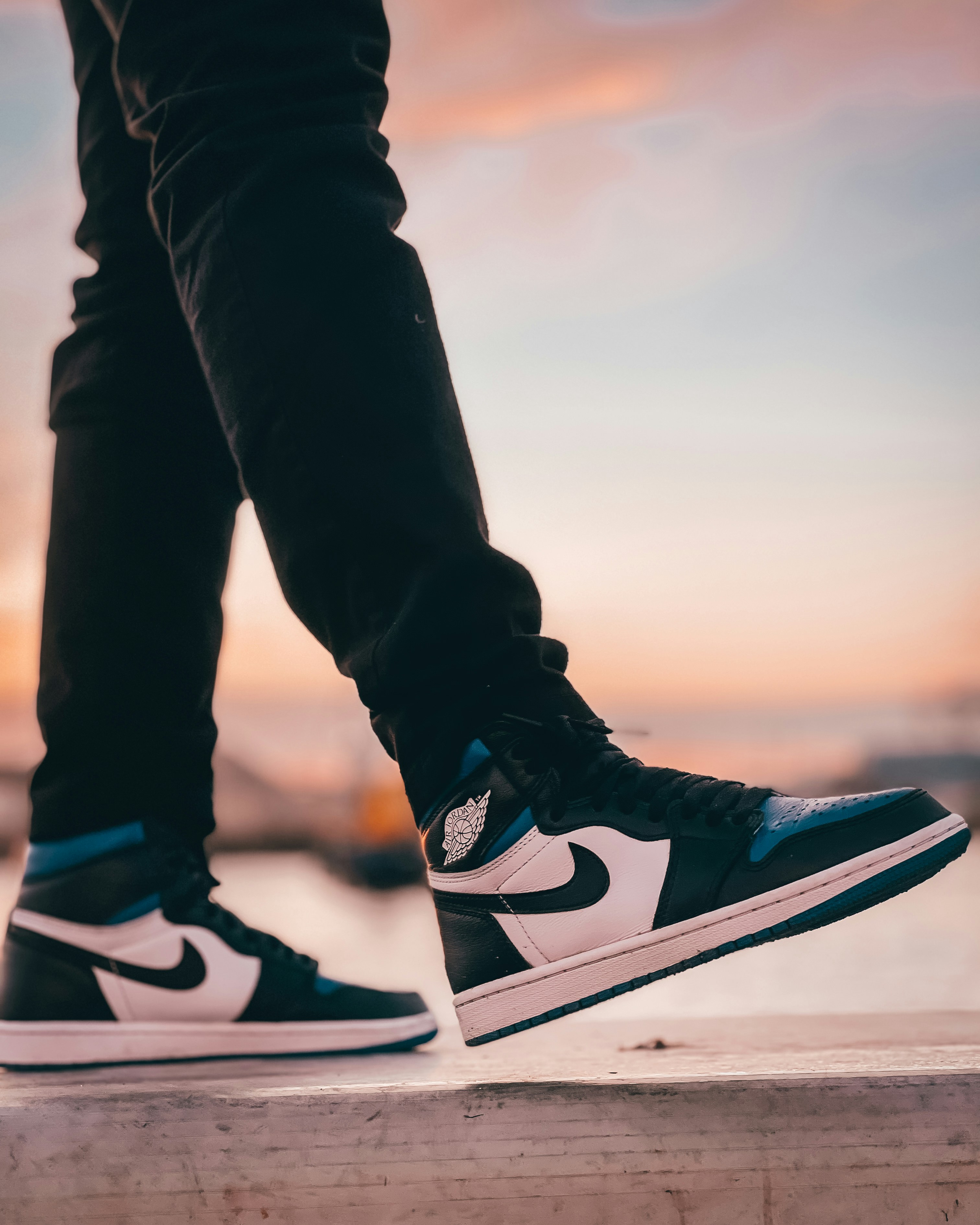 Close-up of a person wearing black and white sneakers against a colorful sunset sky.