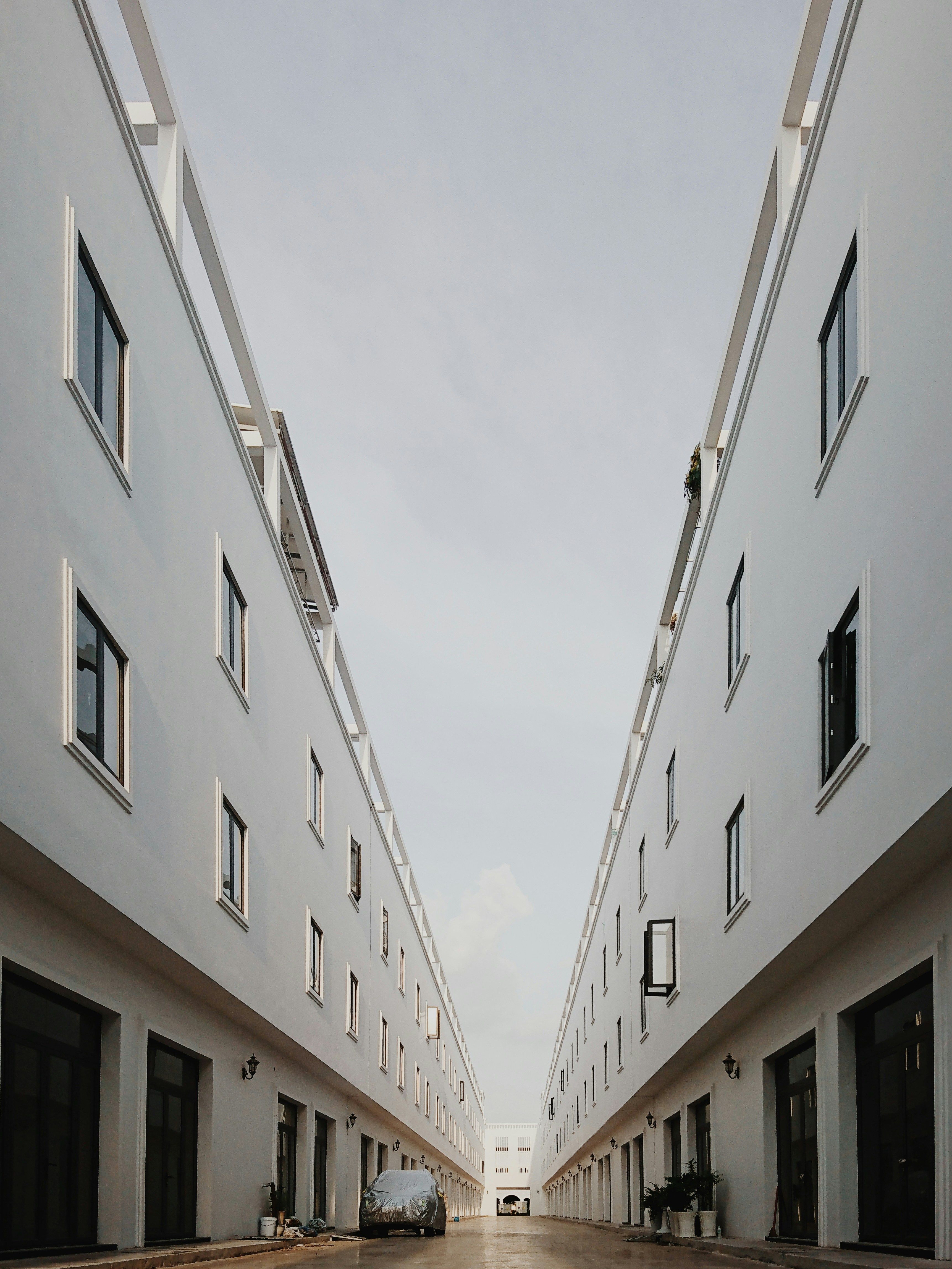 A symmetrical corridor flanked by modern white buildings, leading to a distant entrance under a soft sky. The scene emphasizes architectural lines and minimalistic aesthetics.