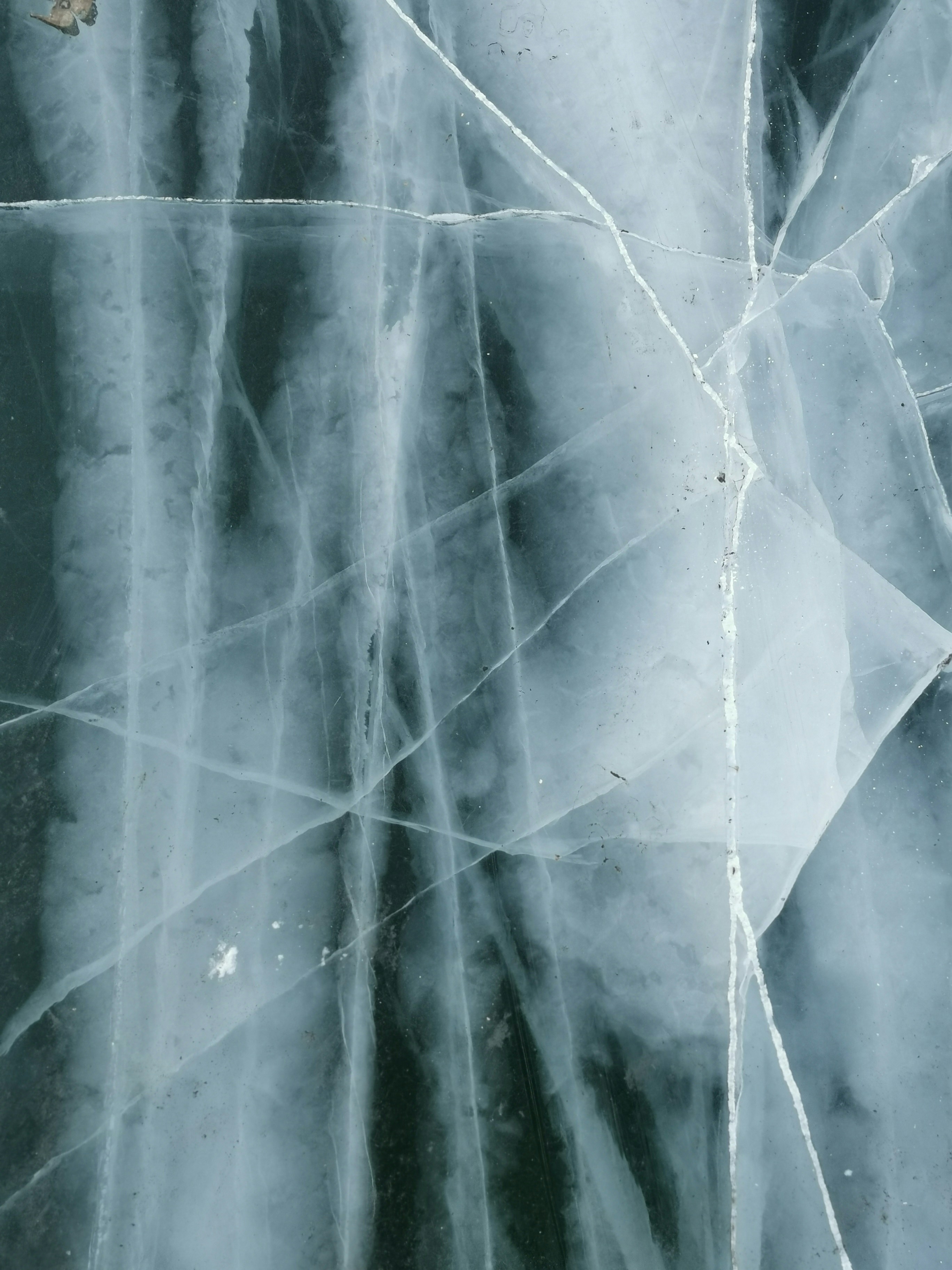 Close-up photograph of blue ice with intersecting fissures and vertical ridges, revealing crystalline texture.