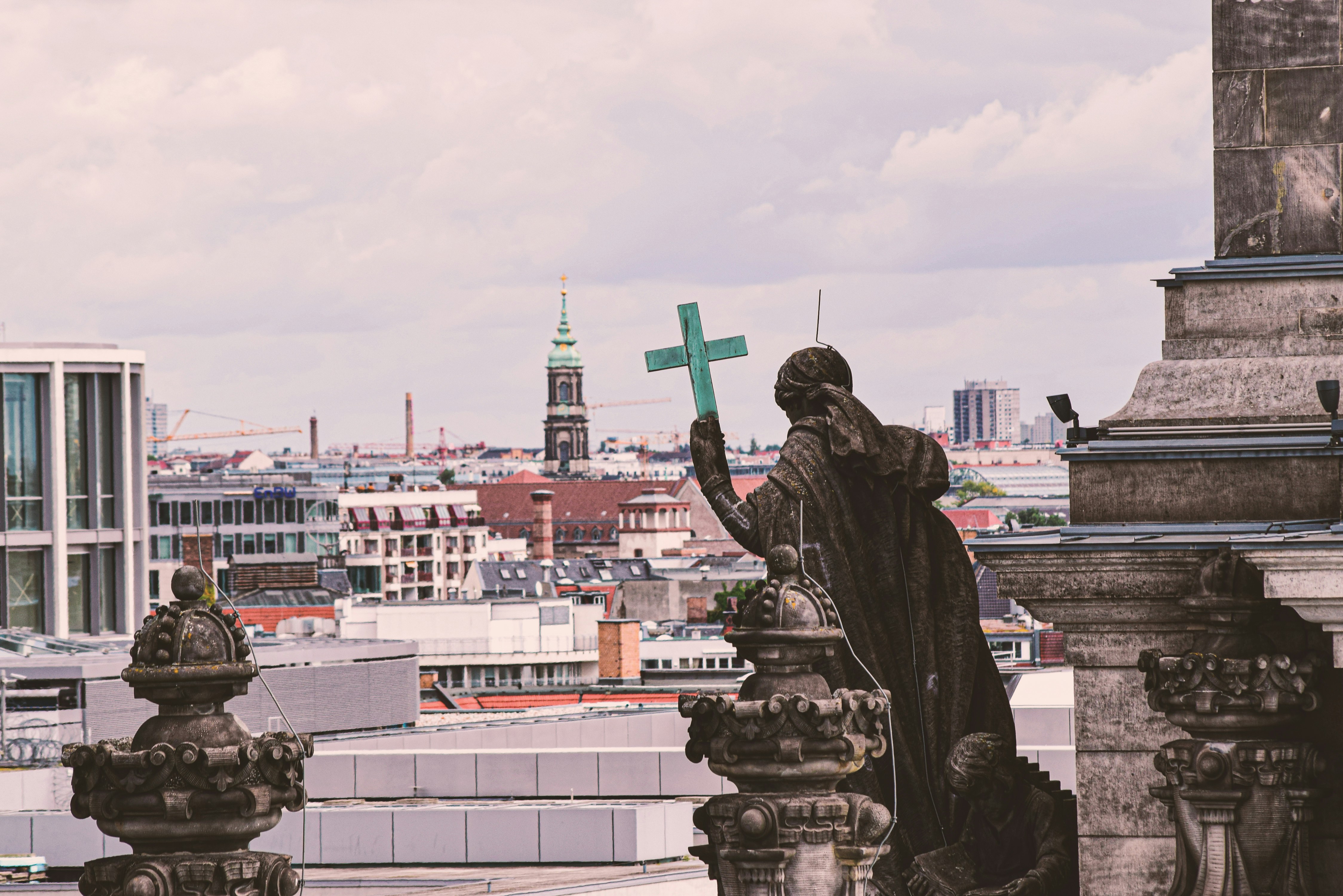 A Cathedral Figure: Cross-bearing Silent Sentinel Over City Rooftops