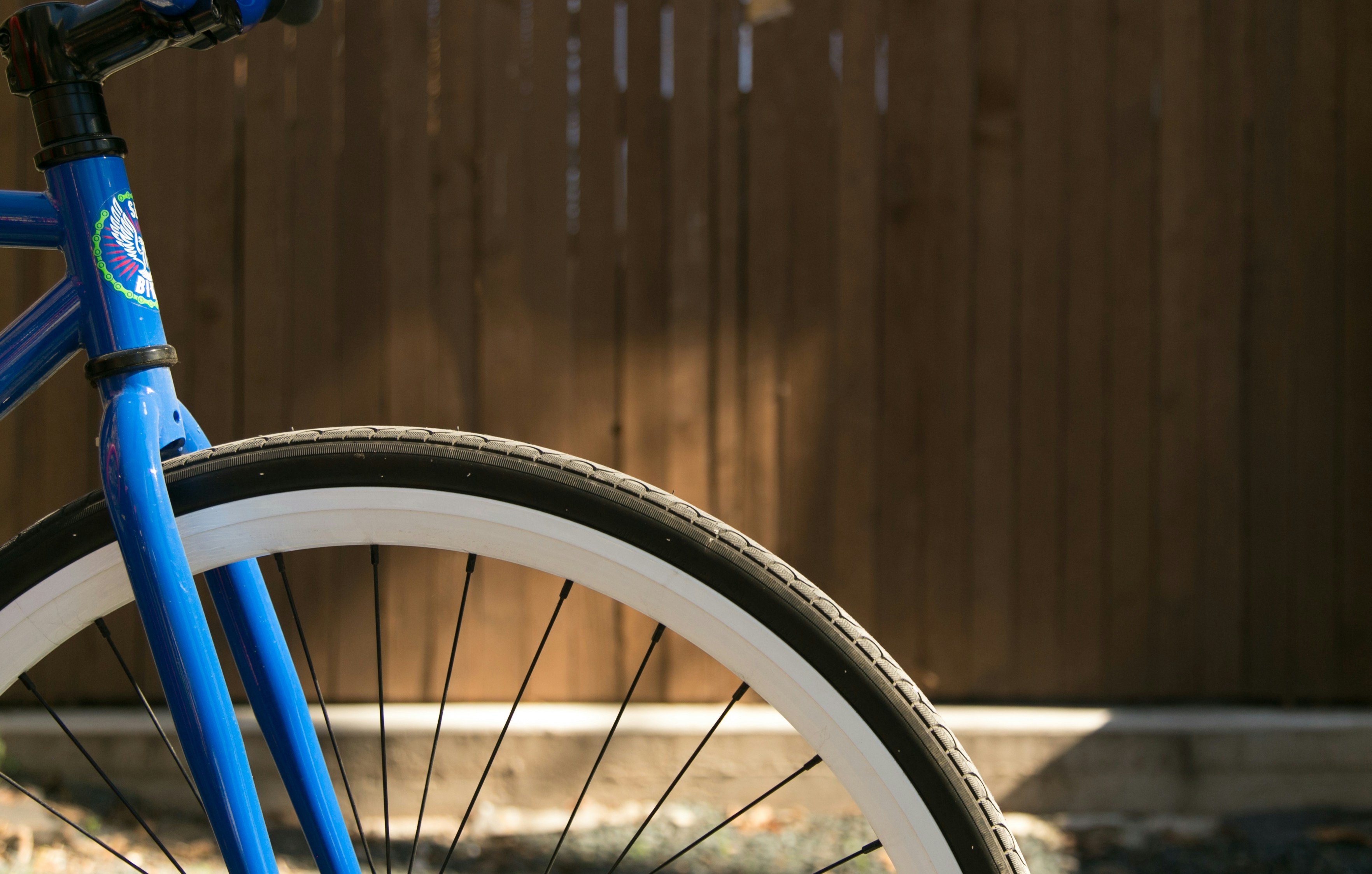 Blue Bicycle Wheel Close-Up: Light on Front Fork Against Weathered Wood