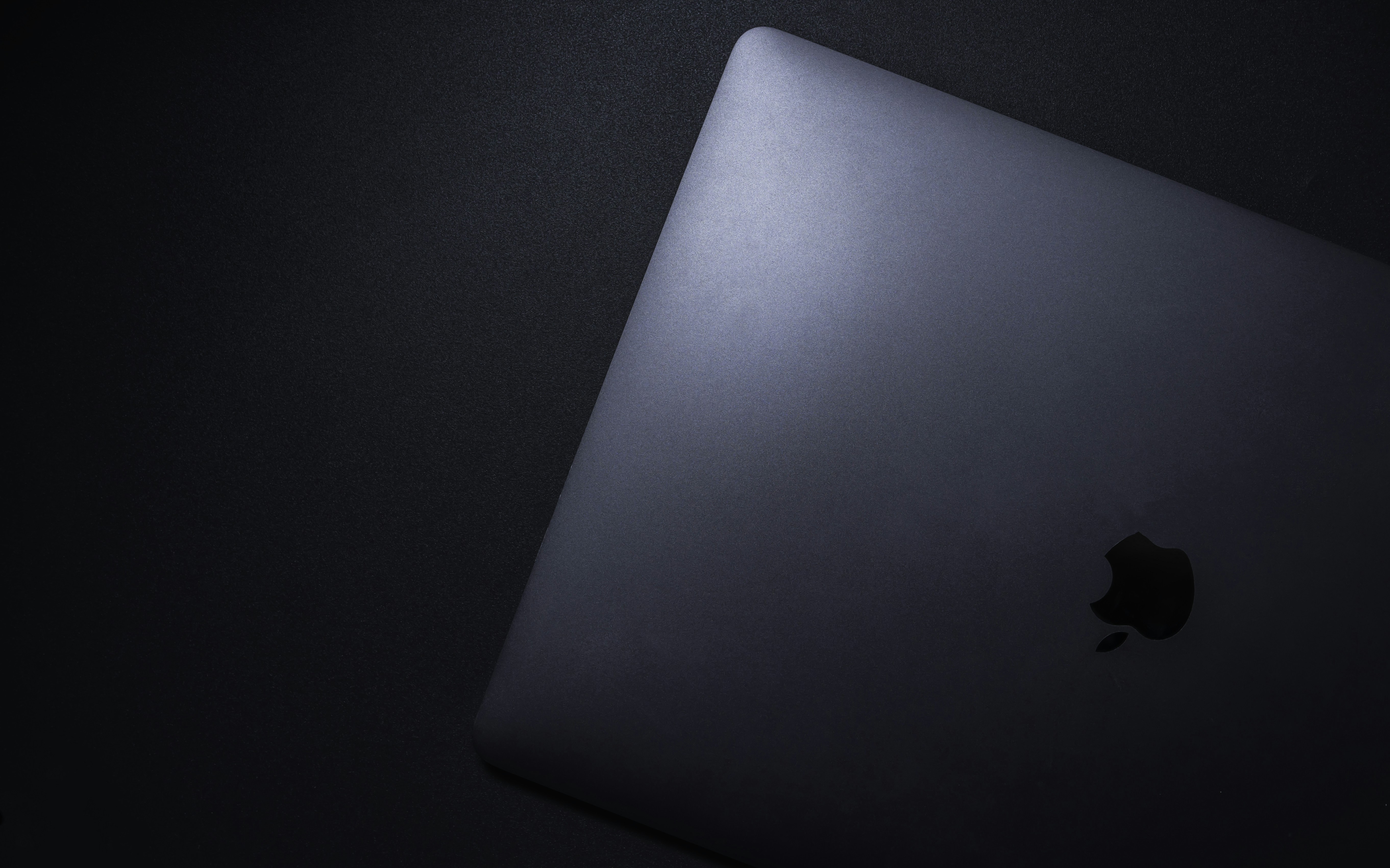 A close-up view of a MacBook laptop resting on a dark surface, illuminated by subtle lighting that highlights its sleek design.