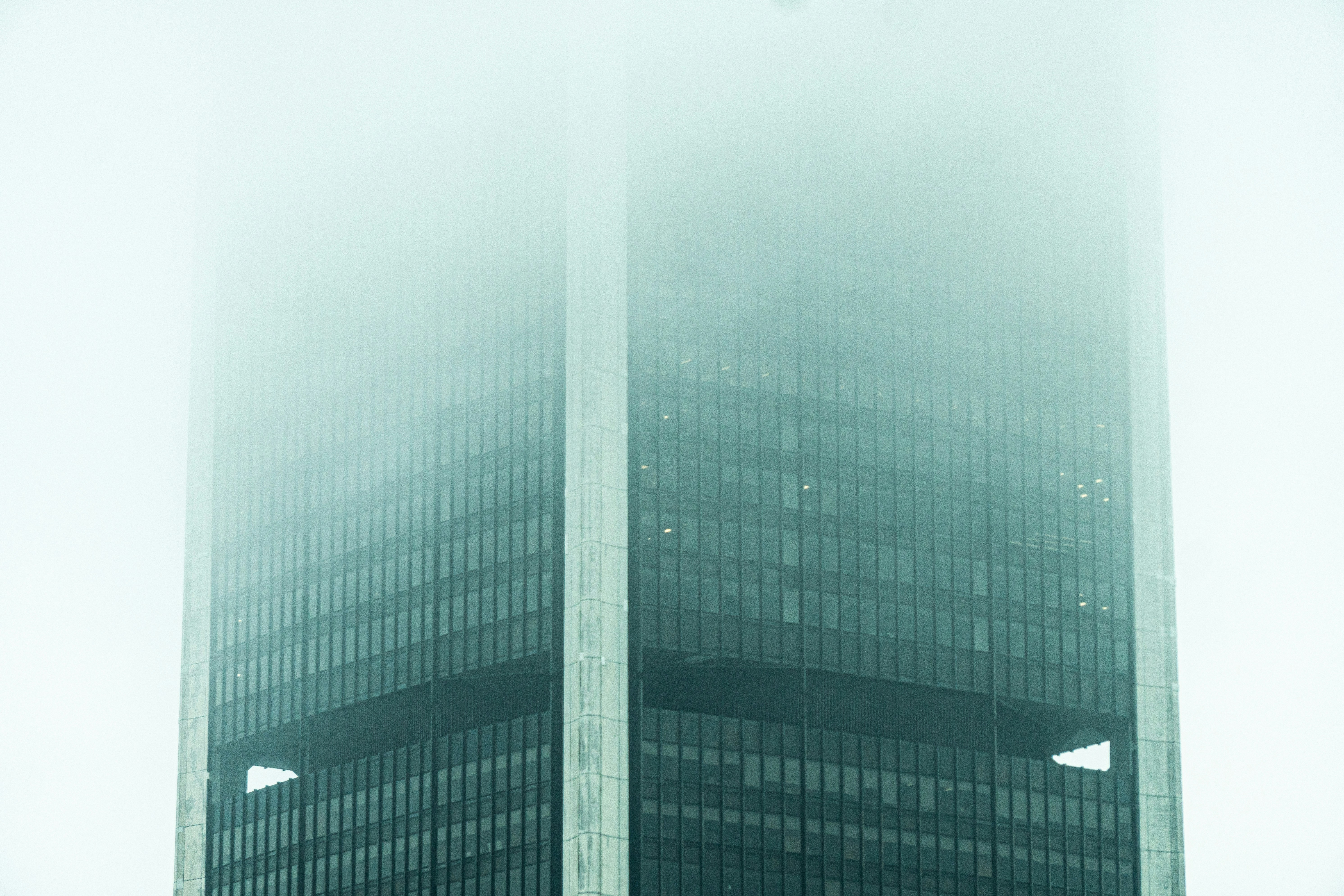 A tall skyscraper partially obscured by fog, revealing its geometric facade and reflective windows. The atmosphere conveys a sense of mystery and urban isolation.