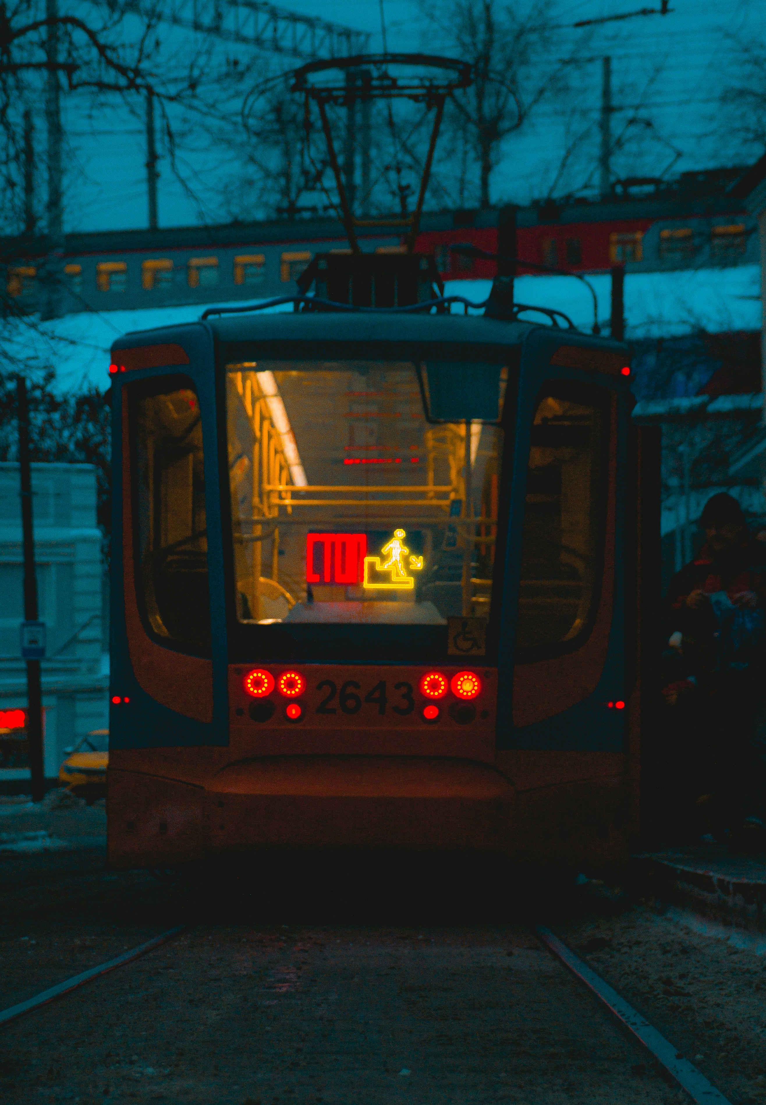 Rear view of a tram with glowing interior lights and a visible sign, set against a twilight backdrop. The scene captures urban transportation in a serene evening atmosphere.
