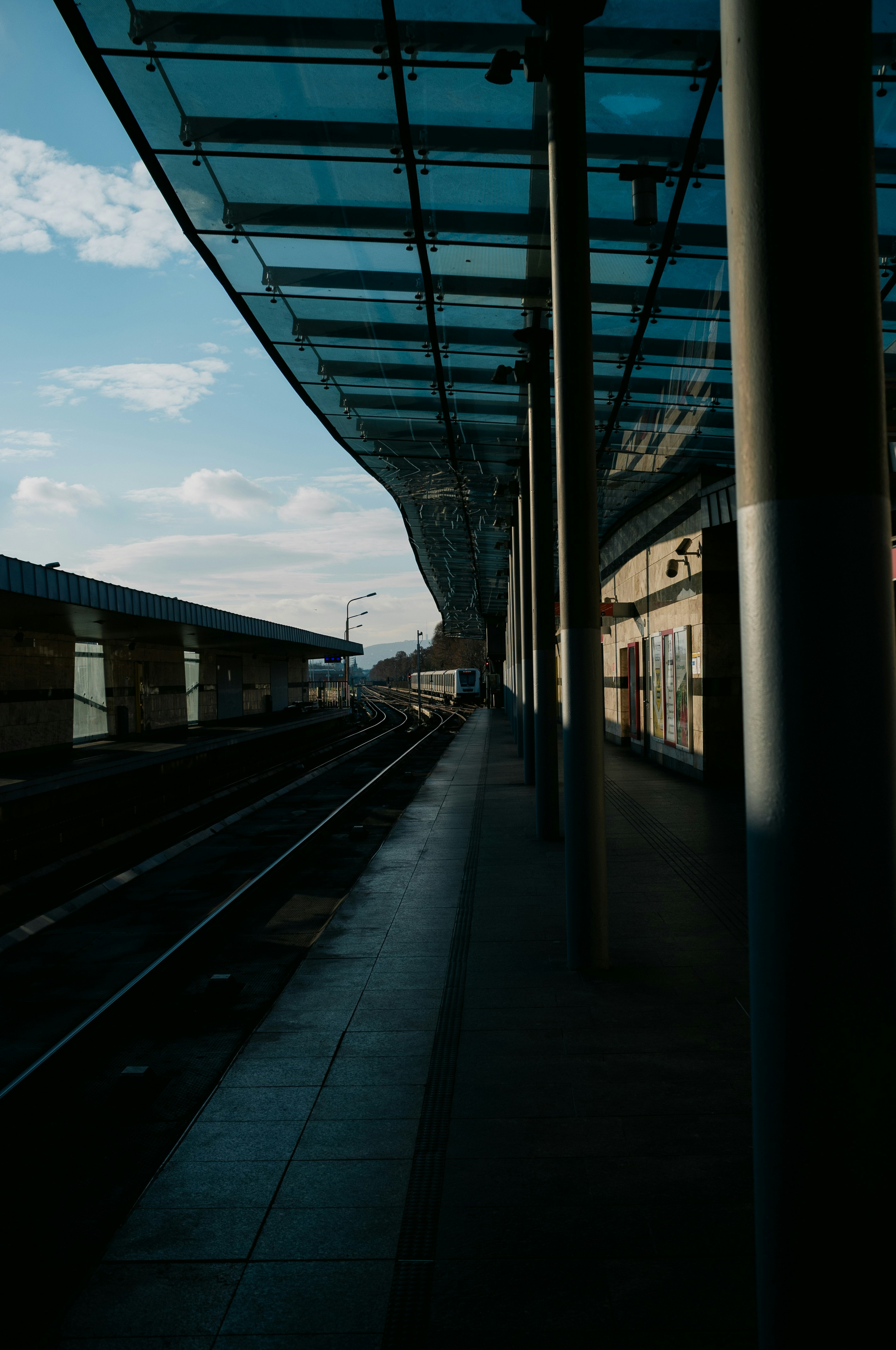Modern train station with sleek glass roof and tracks curving into the distance under a partly cloudy sky.