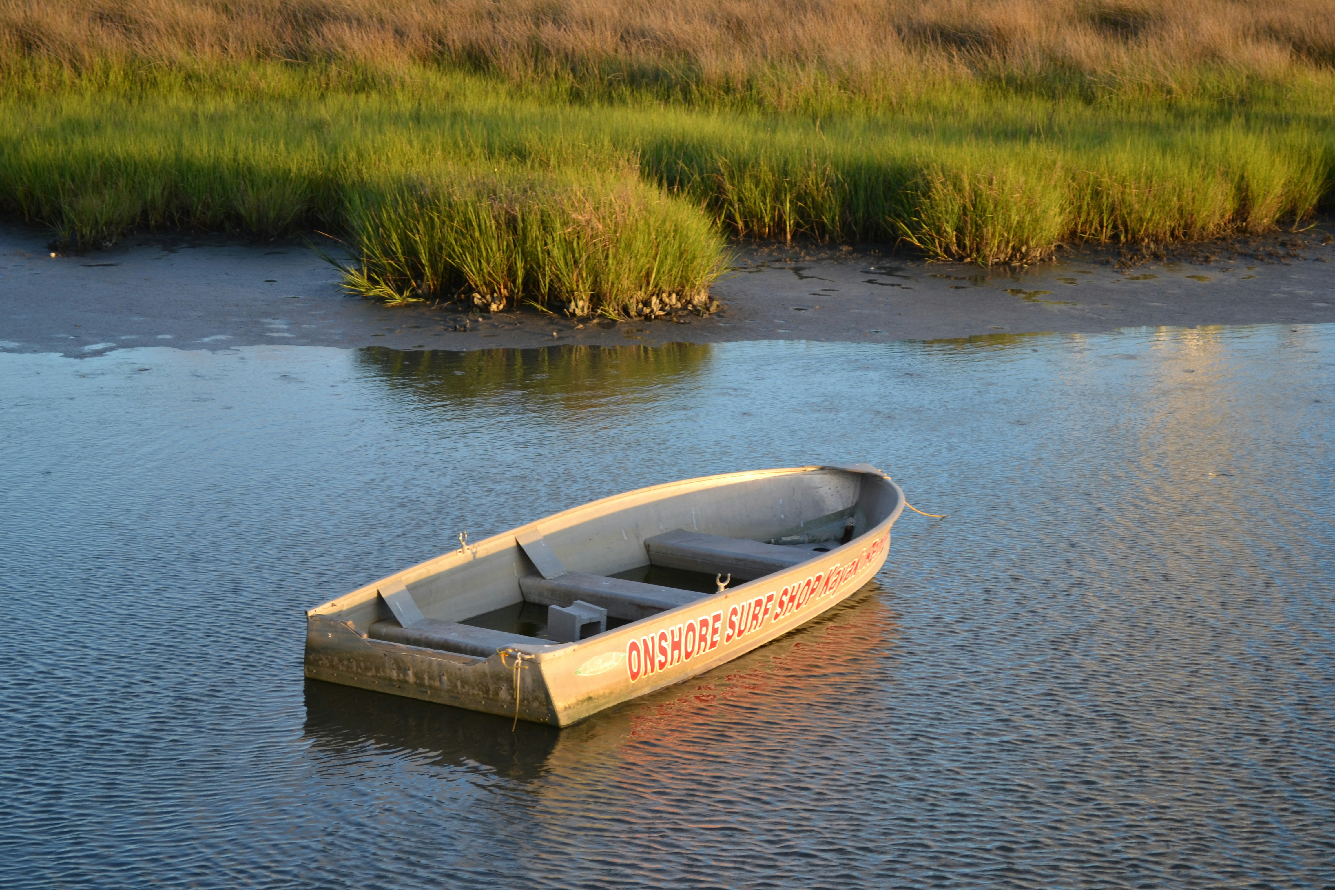 A small boat rests peacefully in calm waters, surrounded by lush green marsh grass under soft evening light.