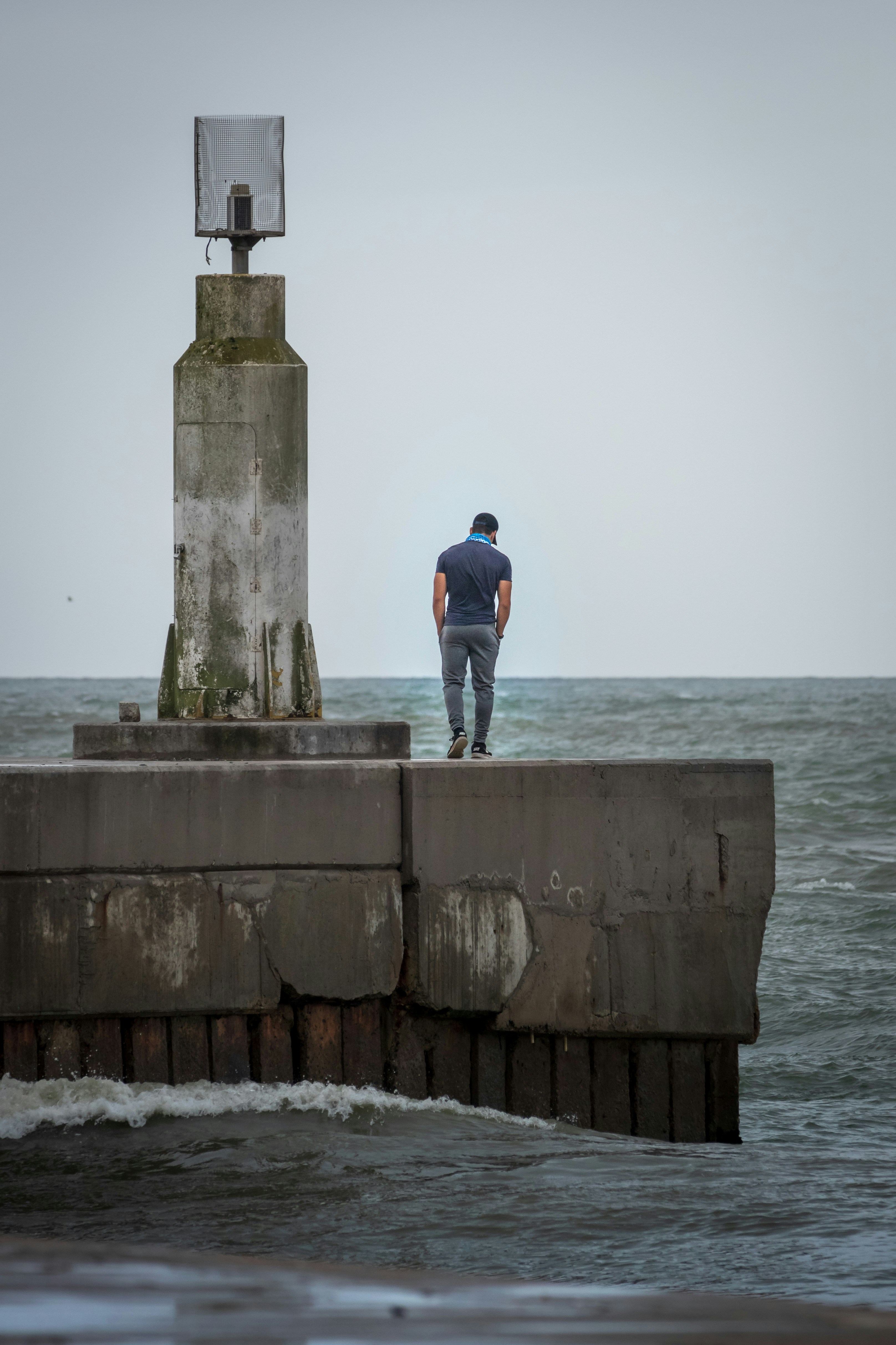 Man standing at the mouth of a river, contemplating the ocean on a cold and windy day.