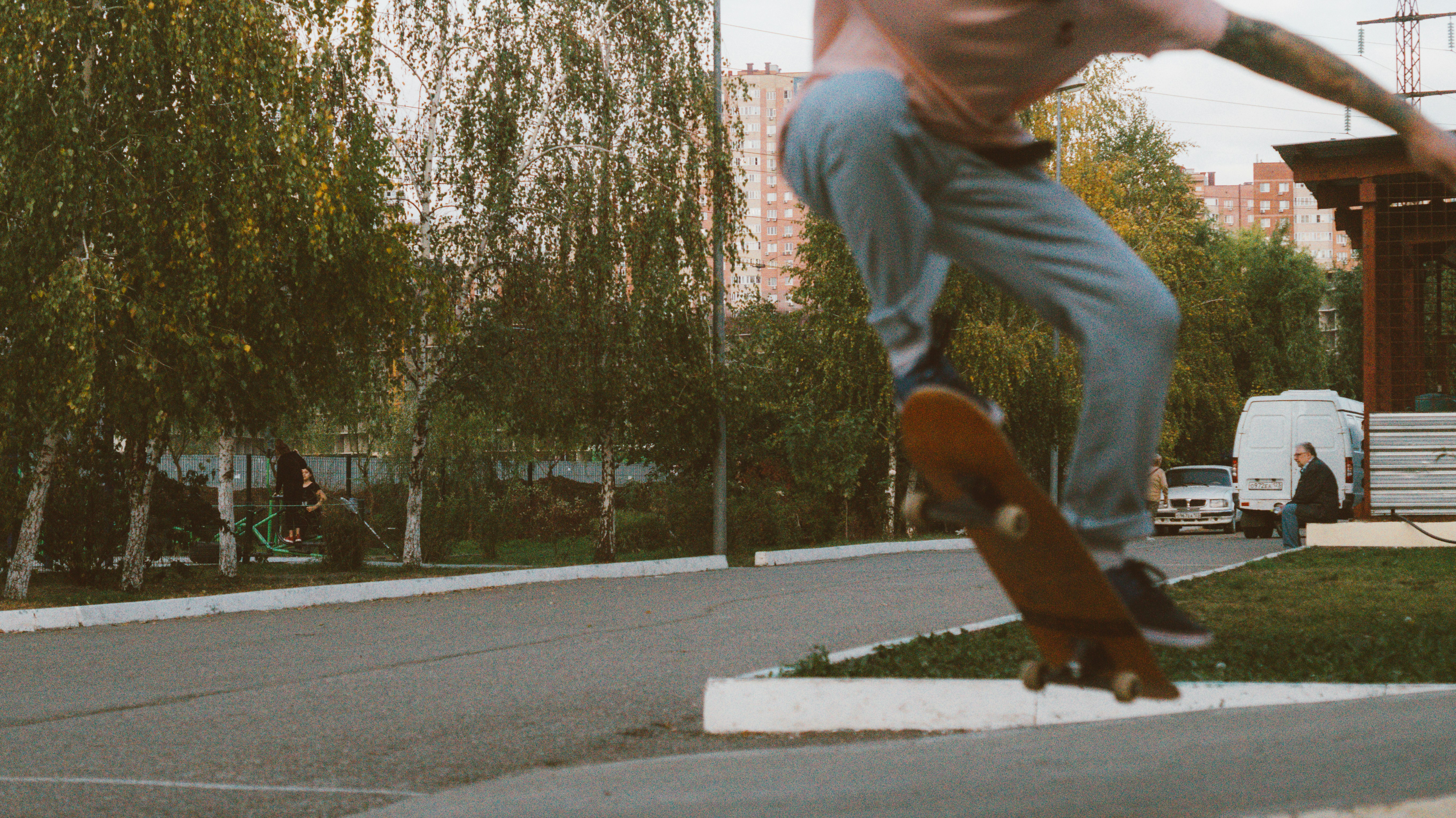 A skateboarder performs a trick mid-air on a smooth pavement surrounded by greenery. The scene captures the essence of urban skate culture.