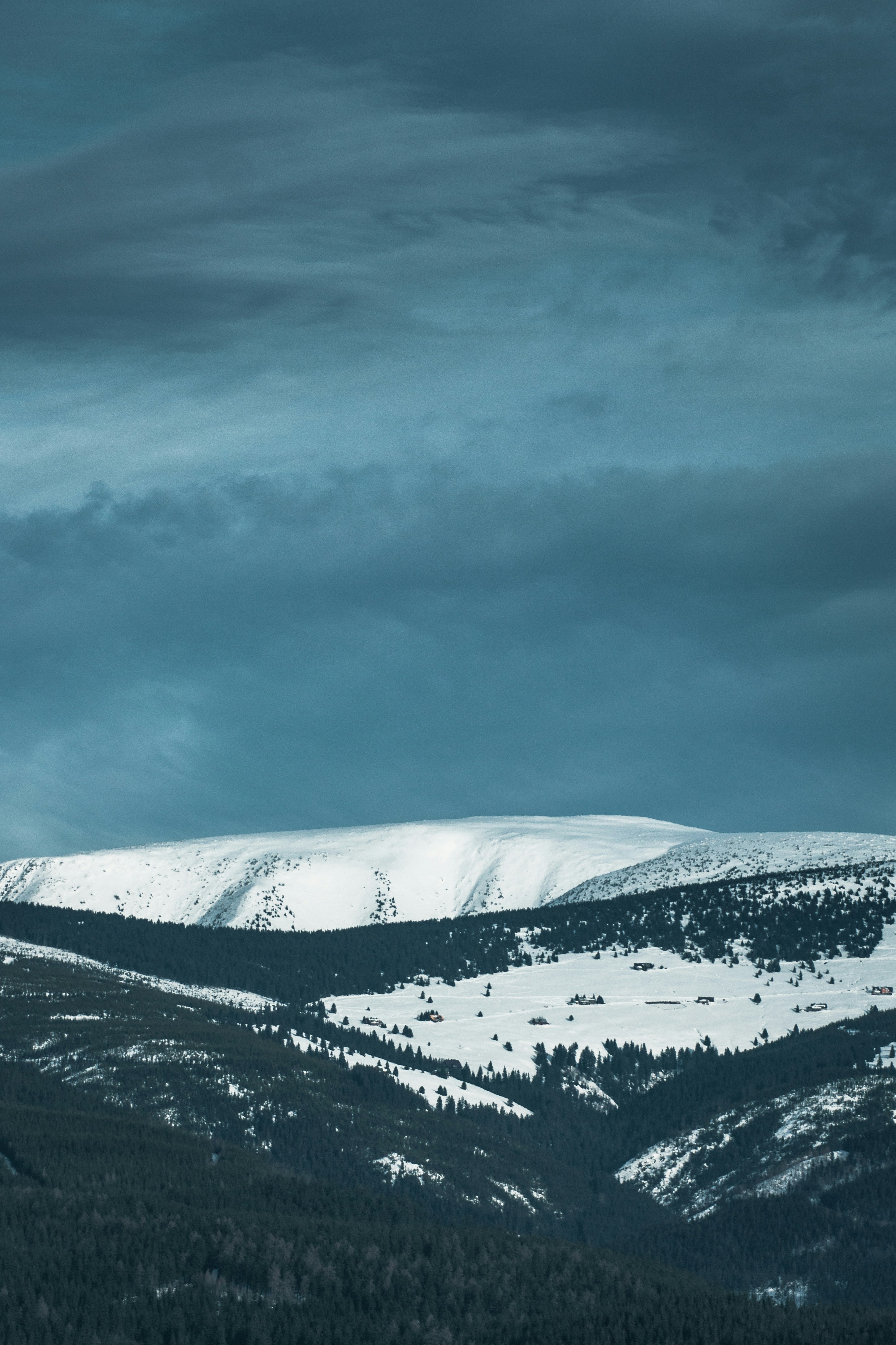 Snow-capped mountains under a moody sky, showcasing the serene beauty of winter landscapes.