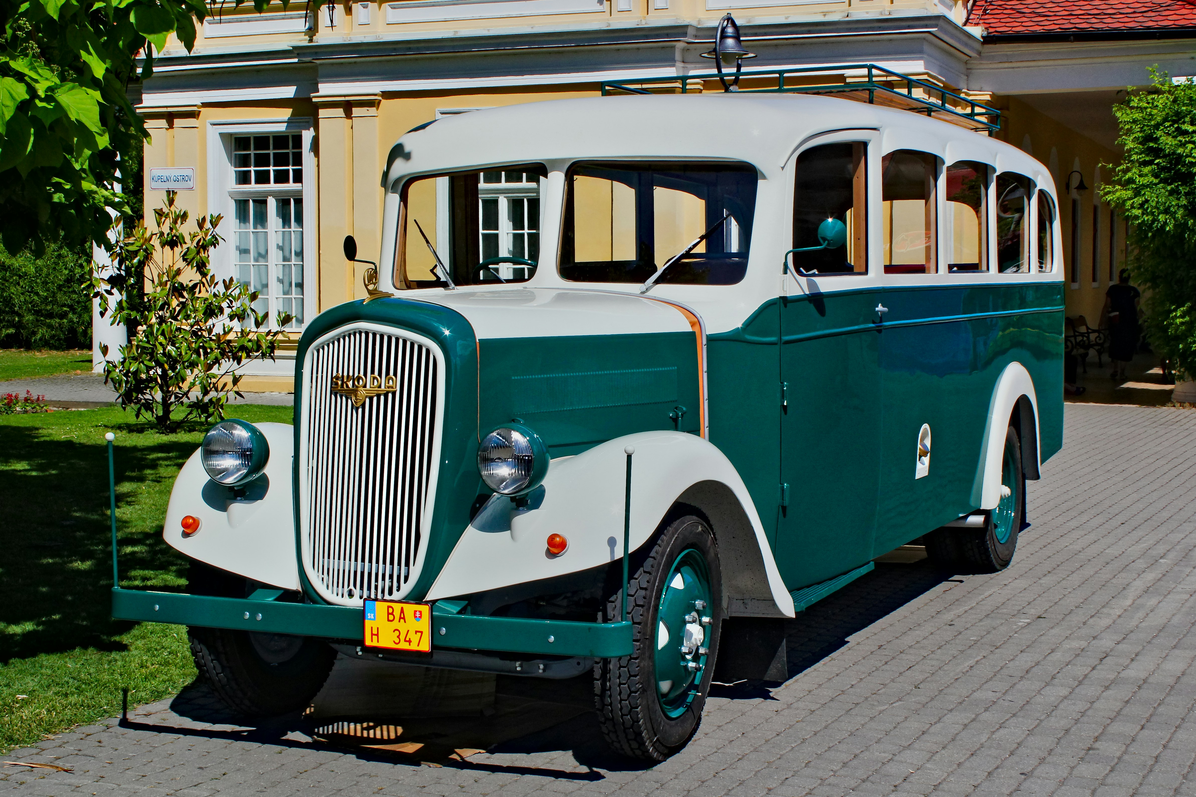 Classic green and white bus parked in front of a historic building, showcasing retro design elements. The vehicle's polished details reflect its well-maintained condition.