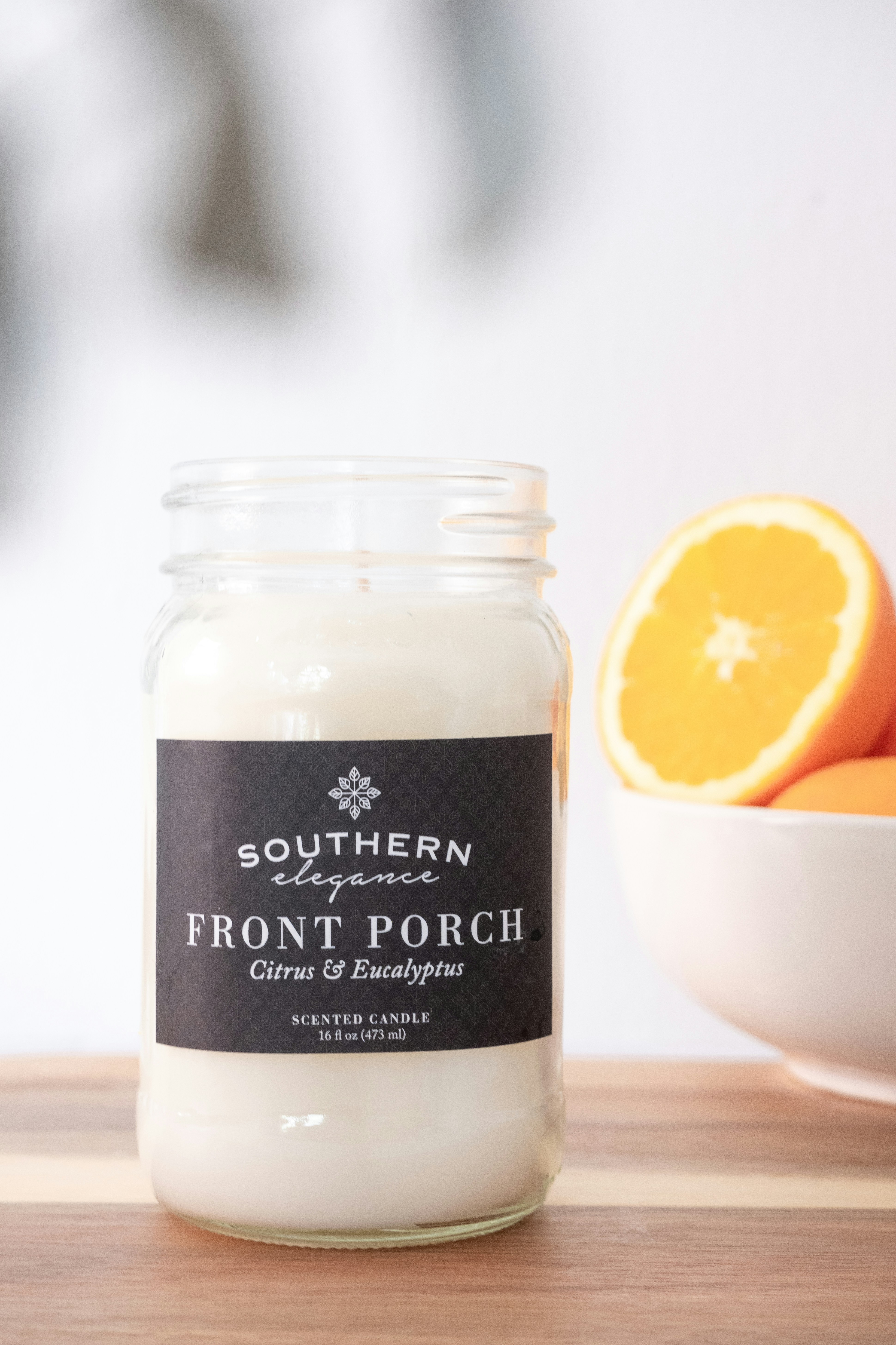 Product shot of candle with foreground and sliced oranges in a bowl.