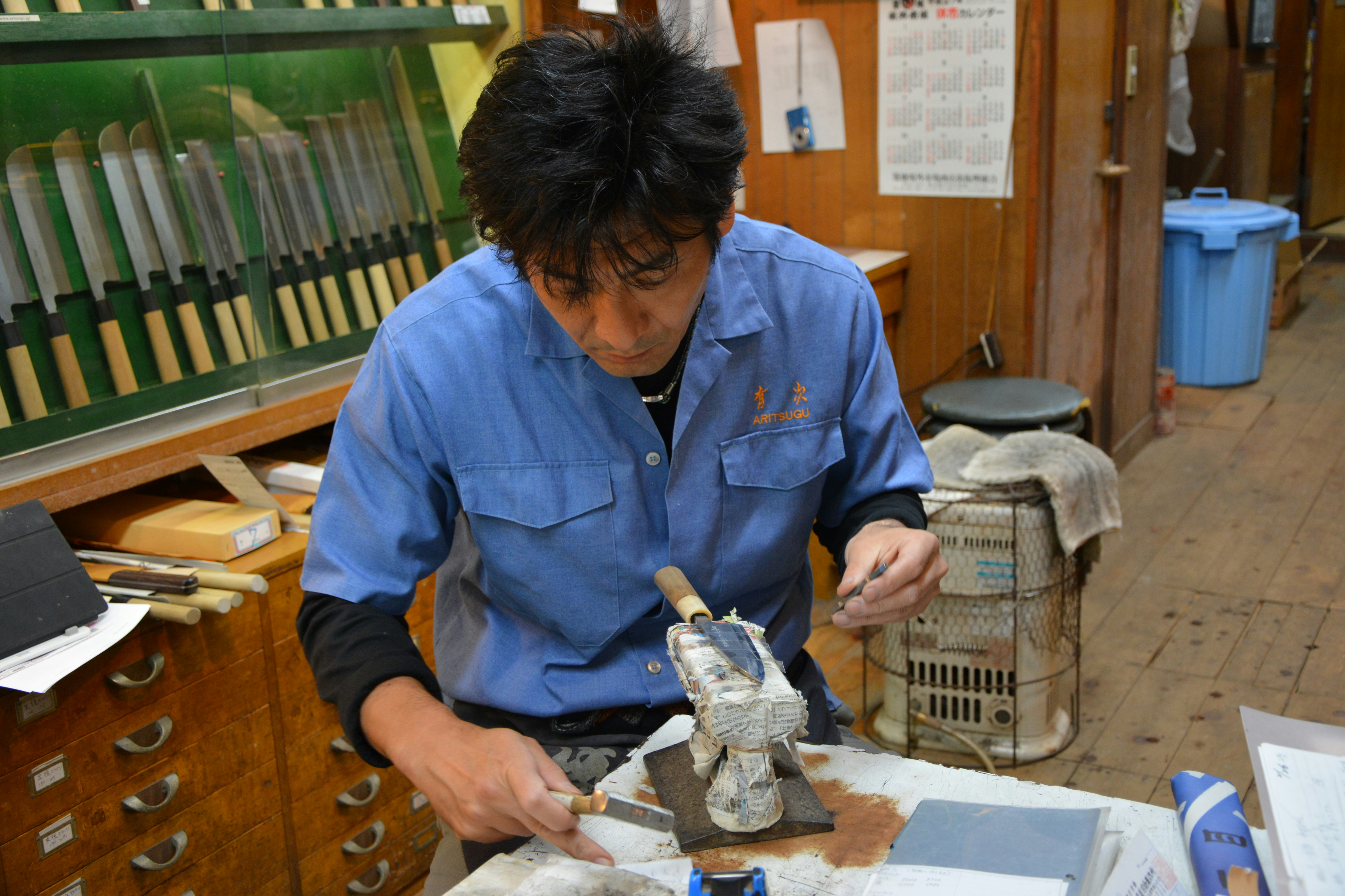 Skilled artisan meticulously sharpening a knife in a traditional workshop, surrounded by tools and materials. The focus is on the craftsmanship involved in knife making.
