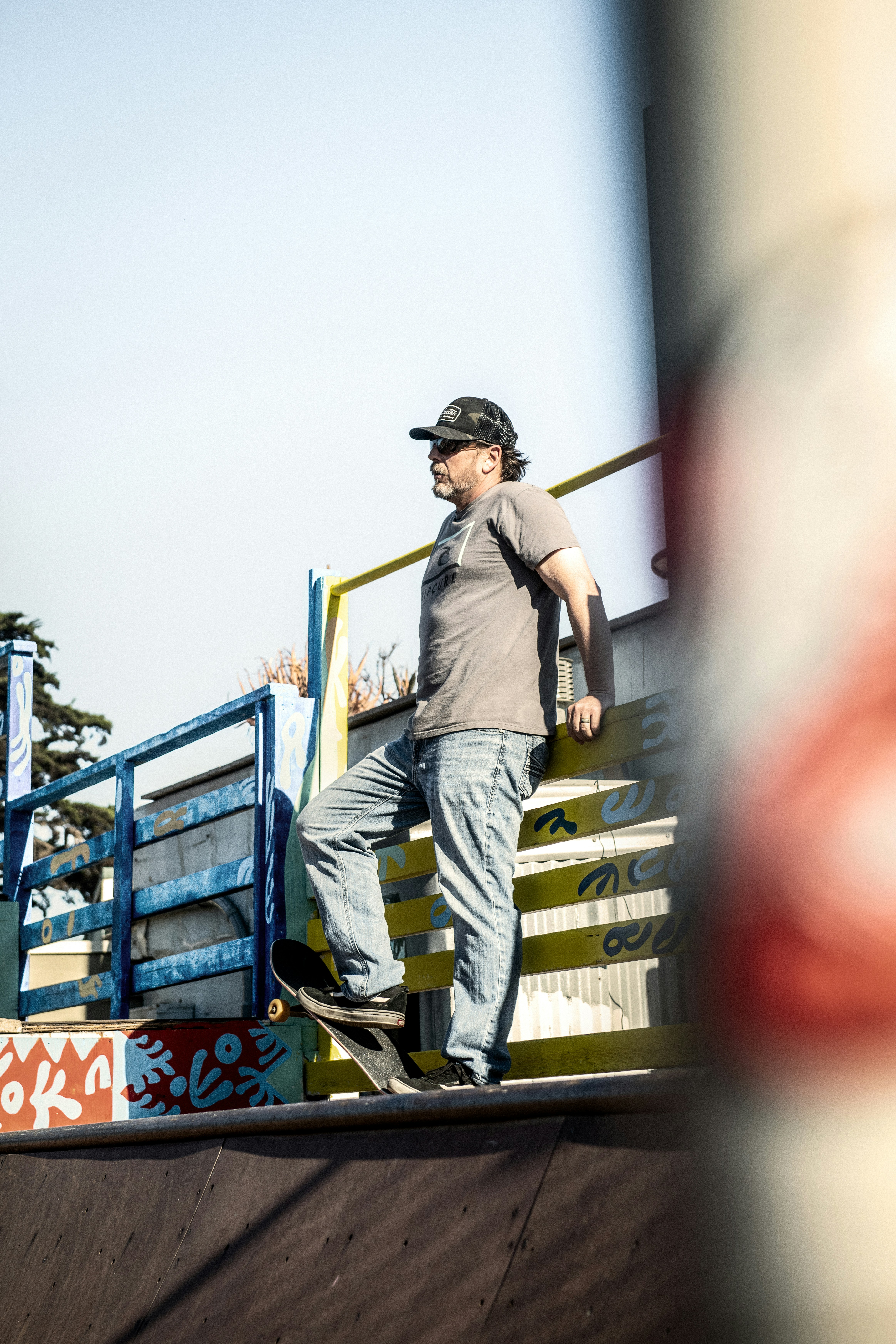 Skateboarder in mid-pinch at sunlit skatepark edge