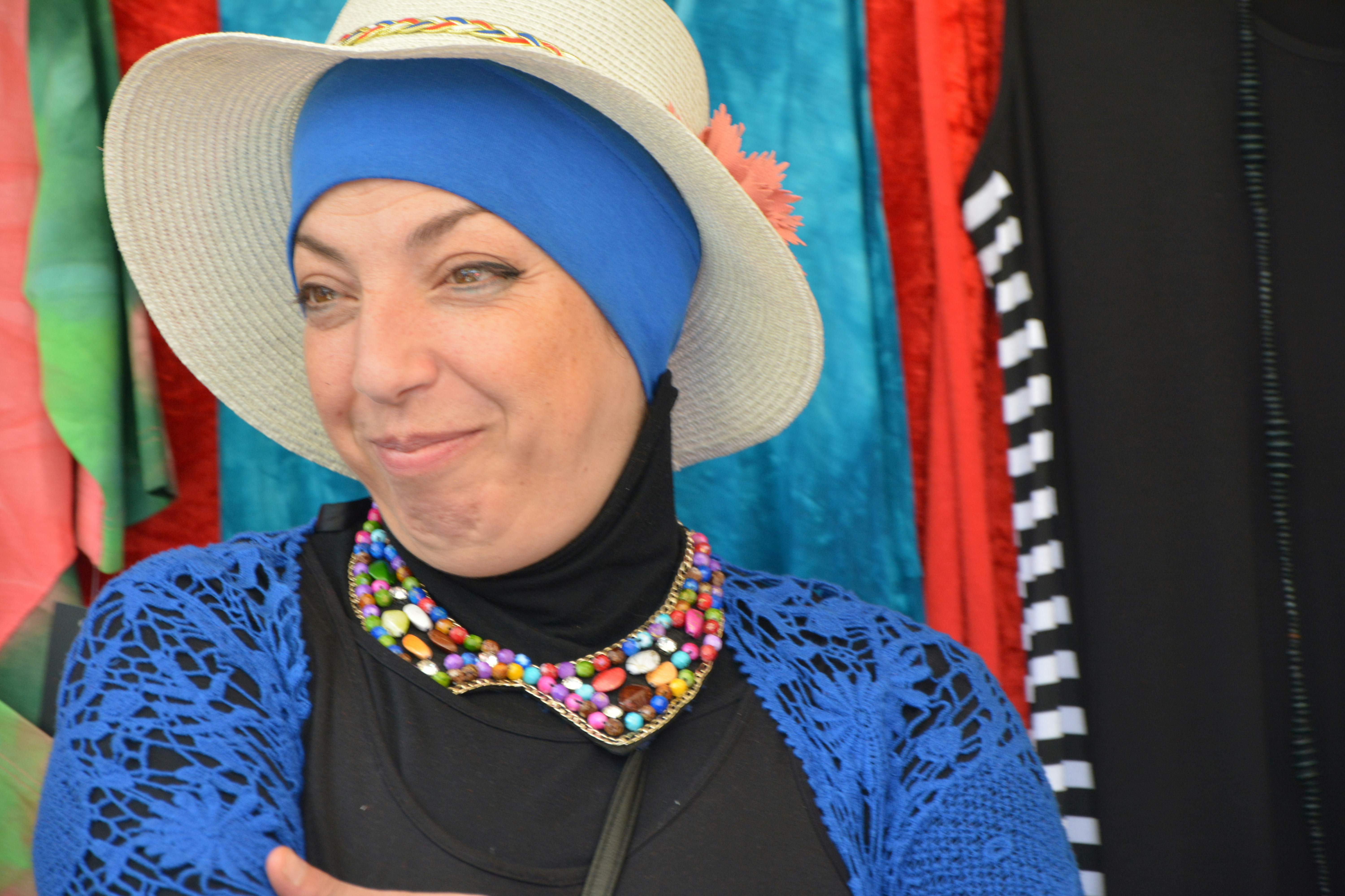Woman wearing colorful jewelry and straw hat manning a both at flea market