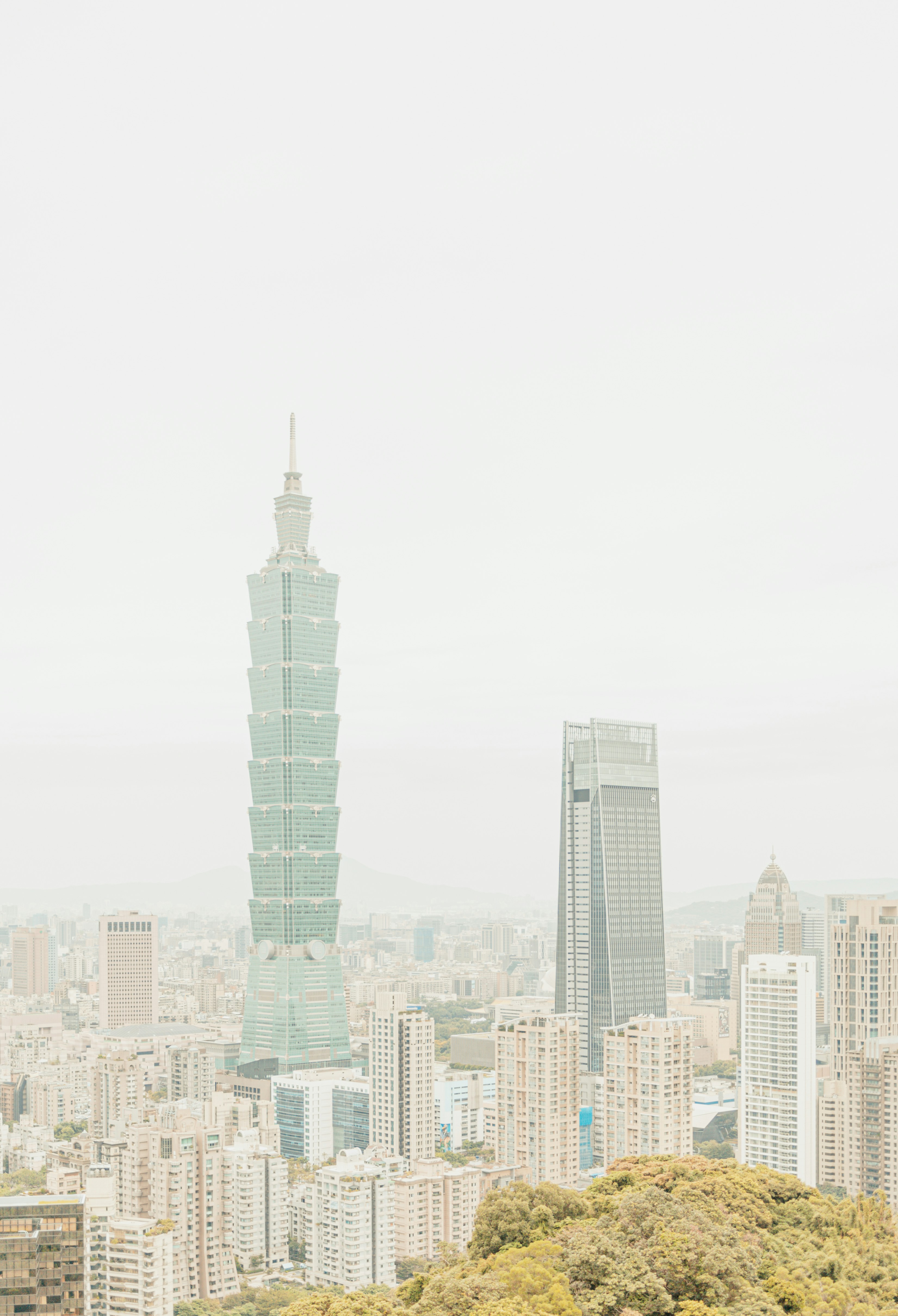 Taipei 101 towers above a sprawling cityscape, enveloped in a soft haze, showcasing modern architecture against a muted backdrop.