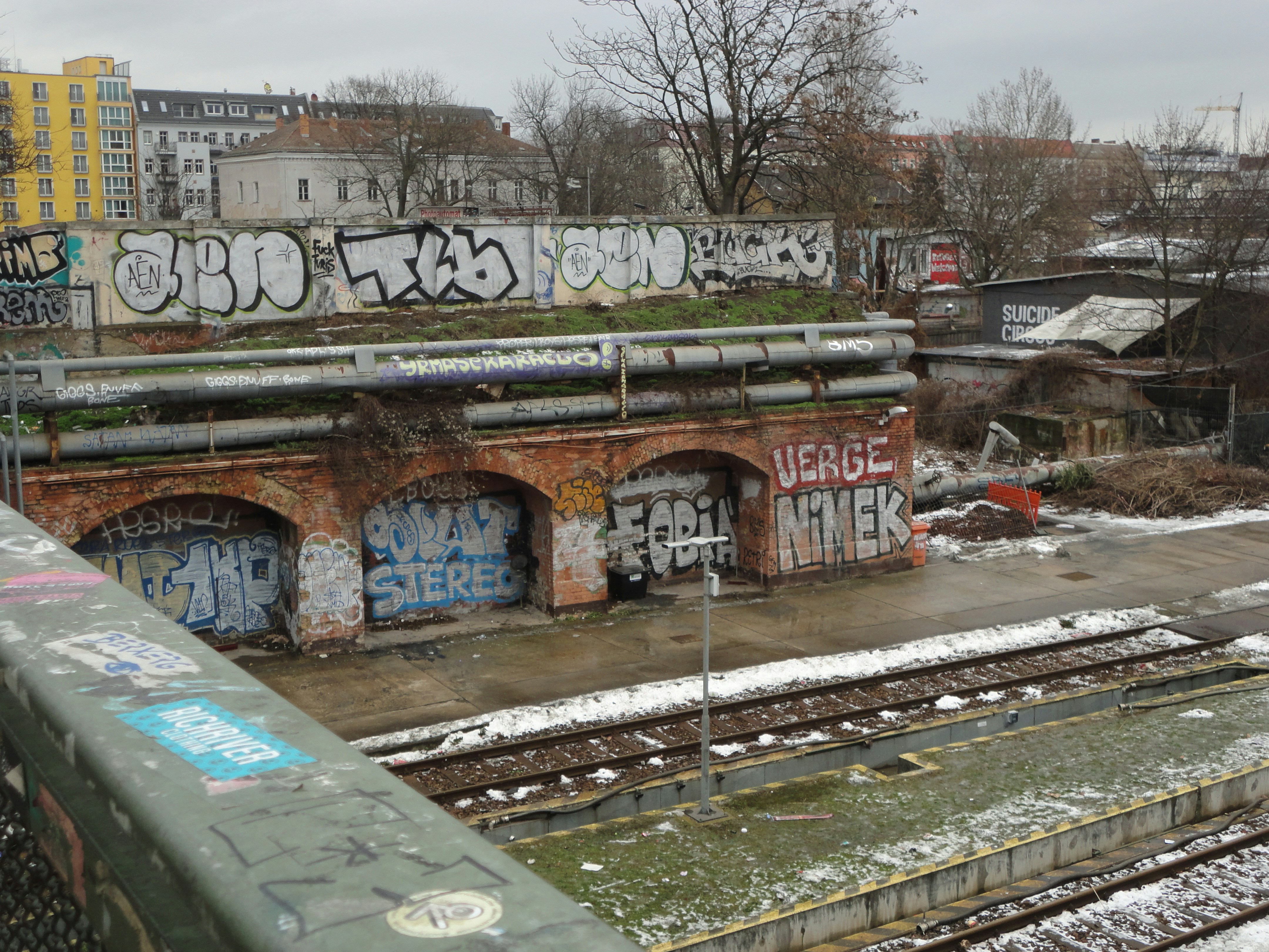 Graffiti-covered brick arches and industrial remnants juxtaposed against a snow-dusted landscape in an urban setting.